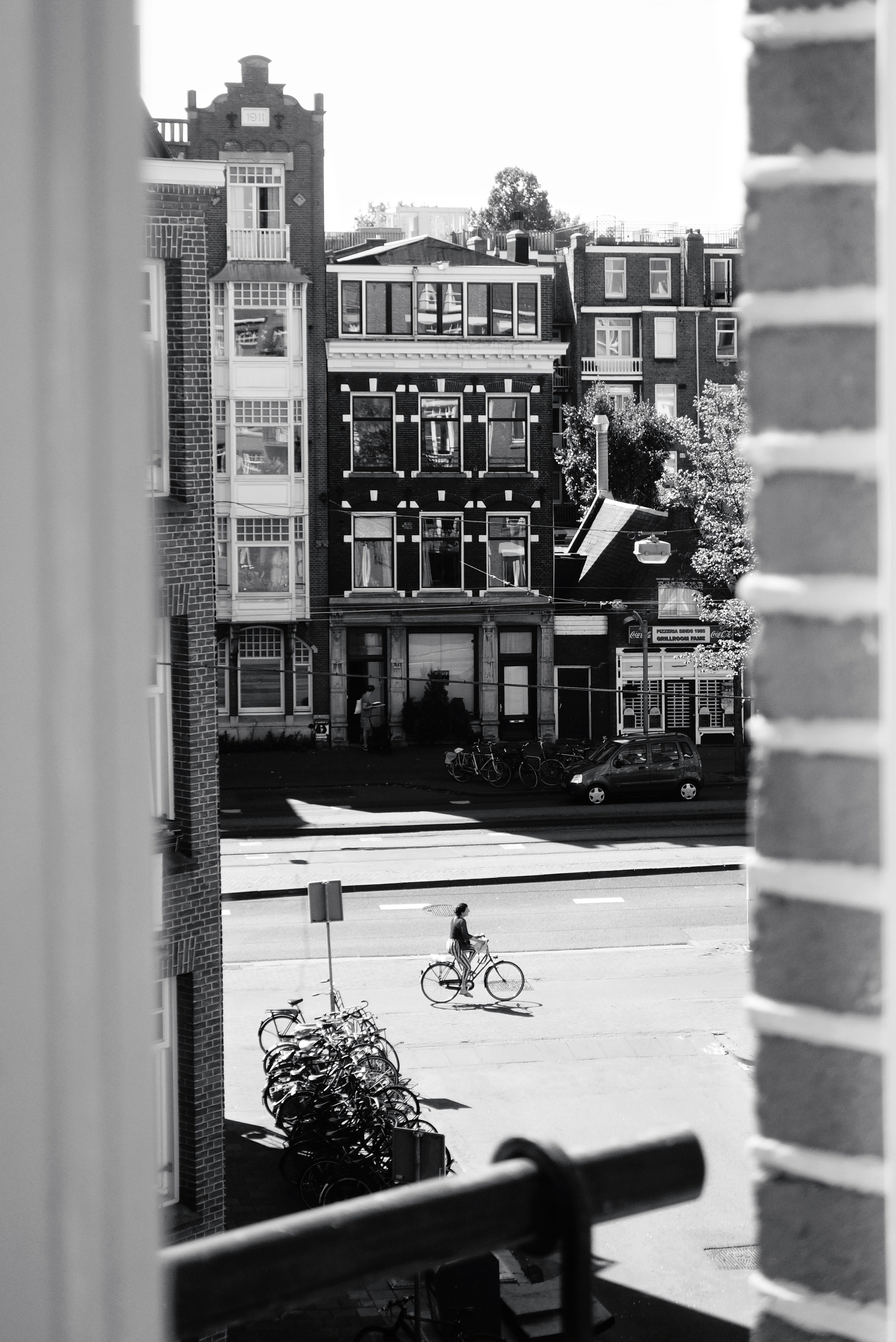A cyclist navigates a city street framed by a window, showcasing a blend of urban architecture and daily life. The scene captures the essence of city living.