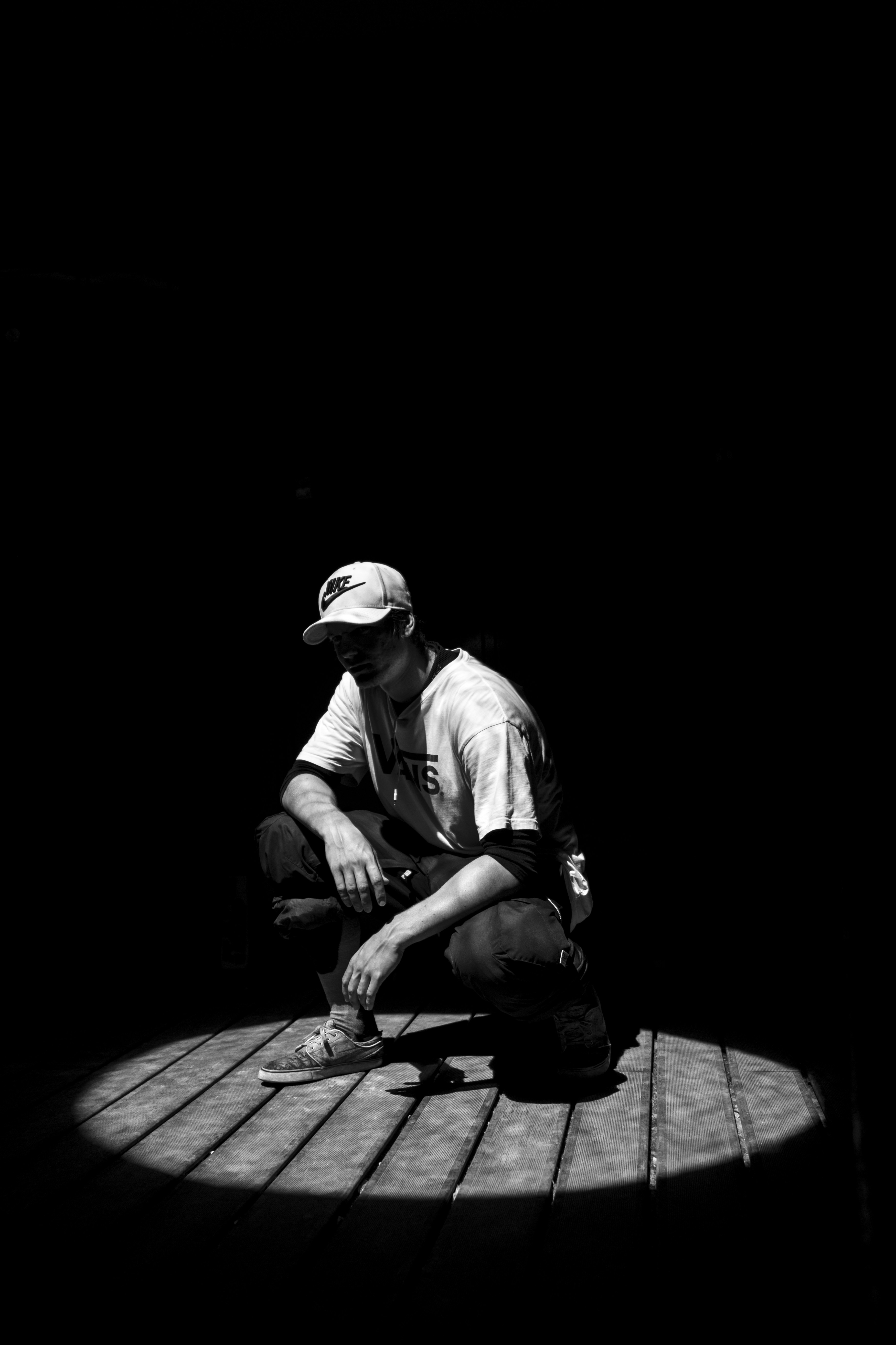 Grayscale photo of a person crouching under a circular beam of light in a dark room.