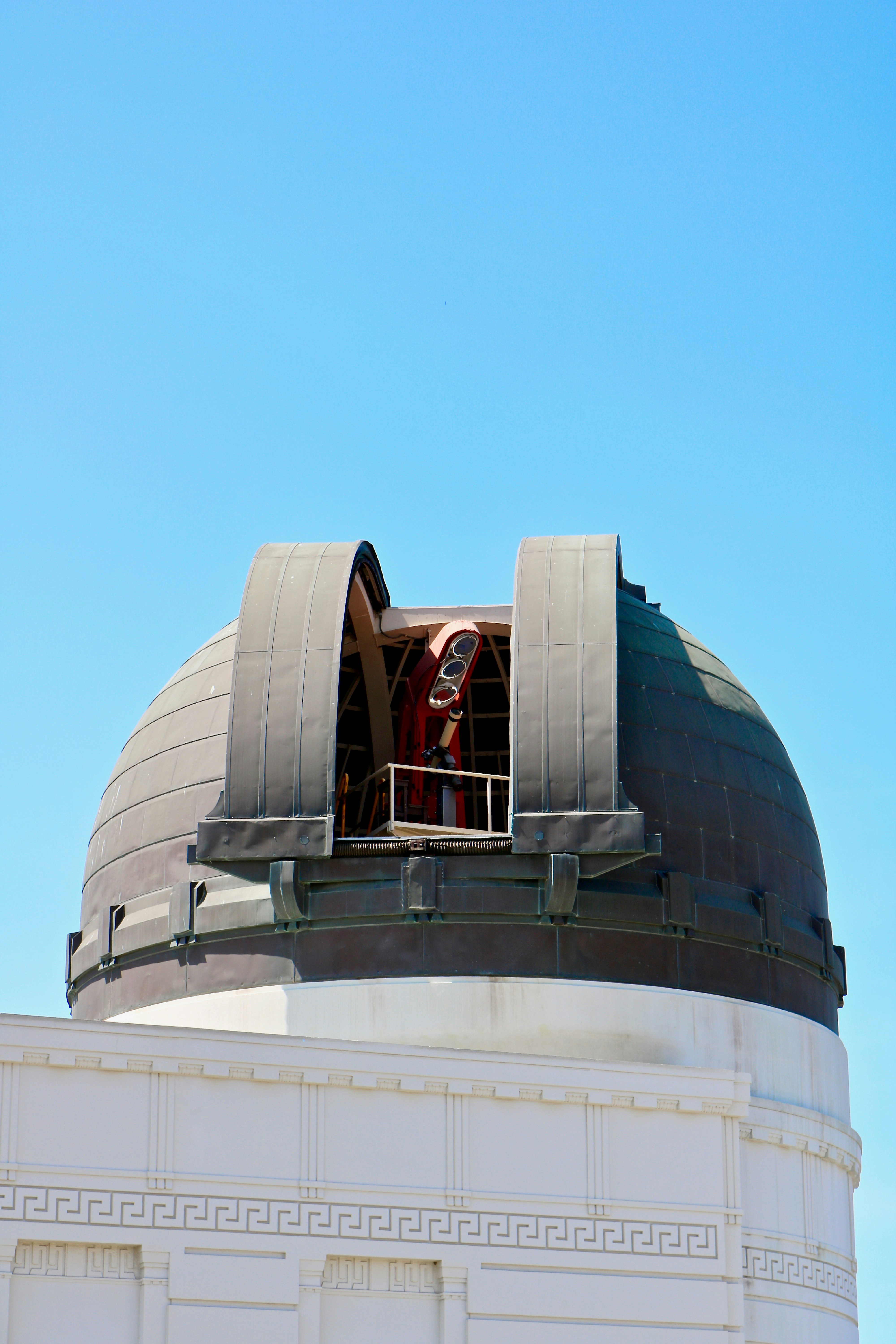 Observatory dome with an open aperture revealing a telescope, set against a clear blue sky.
