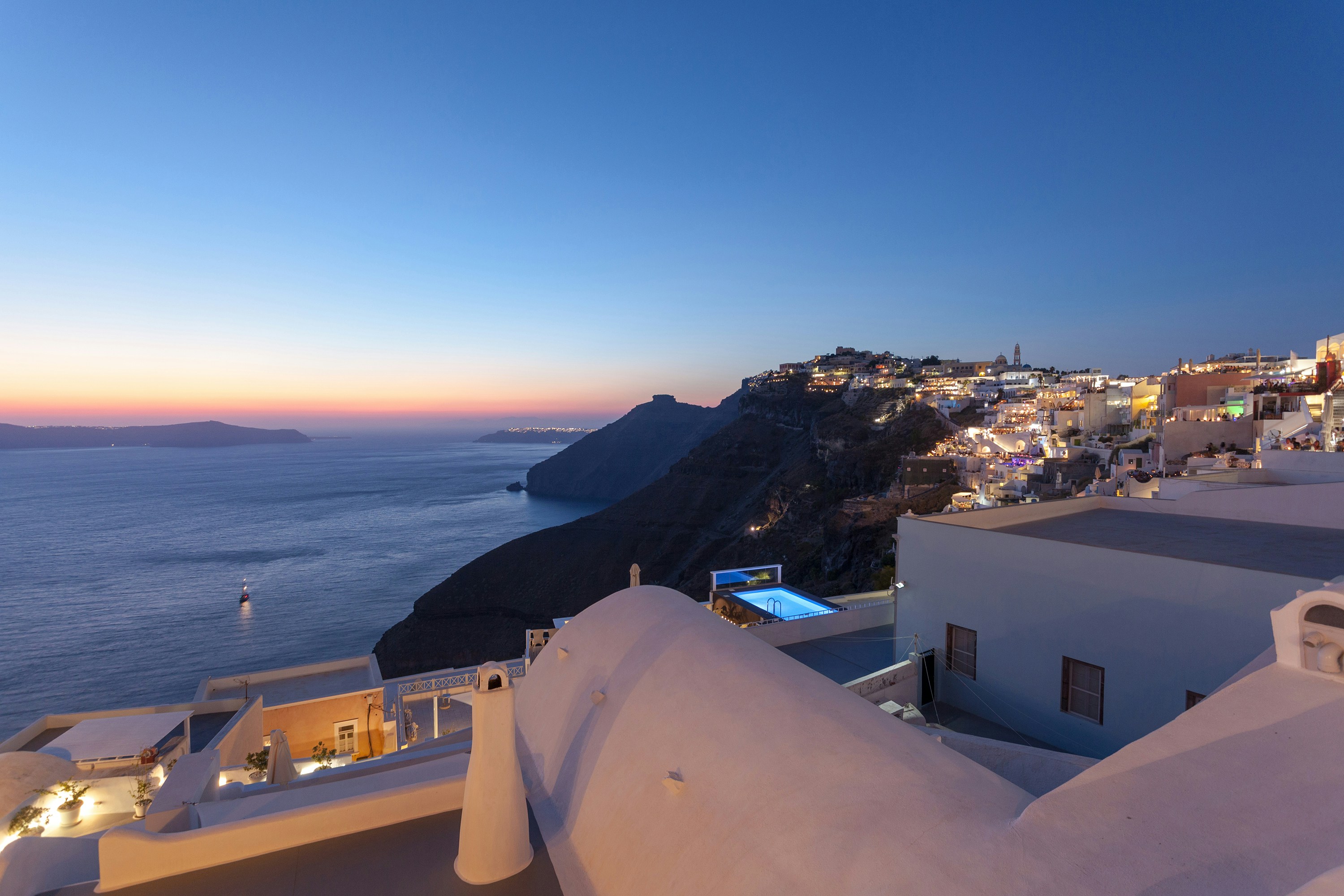 Whitewashed buildings of Santorini illuminated at dusk, overlooking the Aegean Sea.