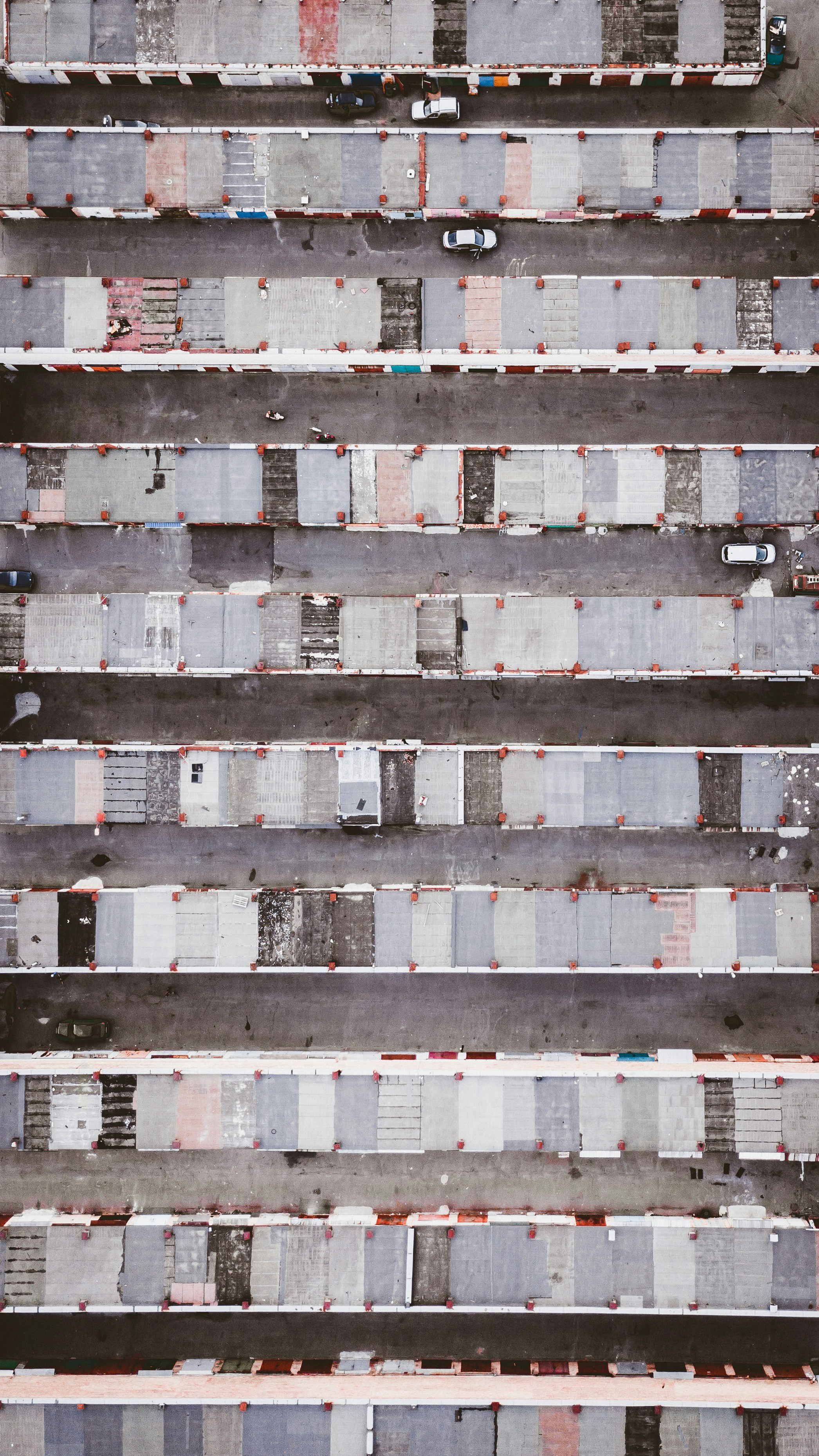 An overhead view of a densely packed parking area, showcasing rows of vehicles and uniform structures. The geometric arrangement highlights the organized chaos of urban life.