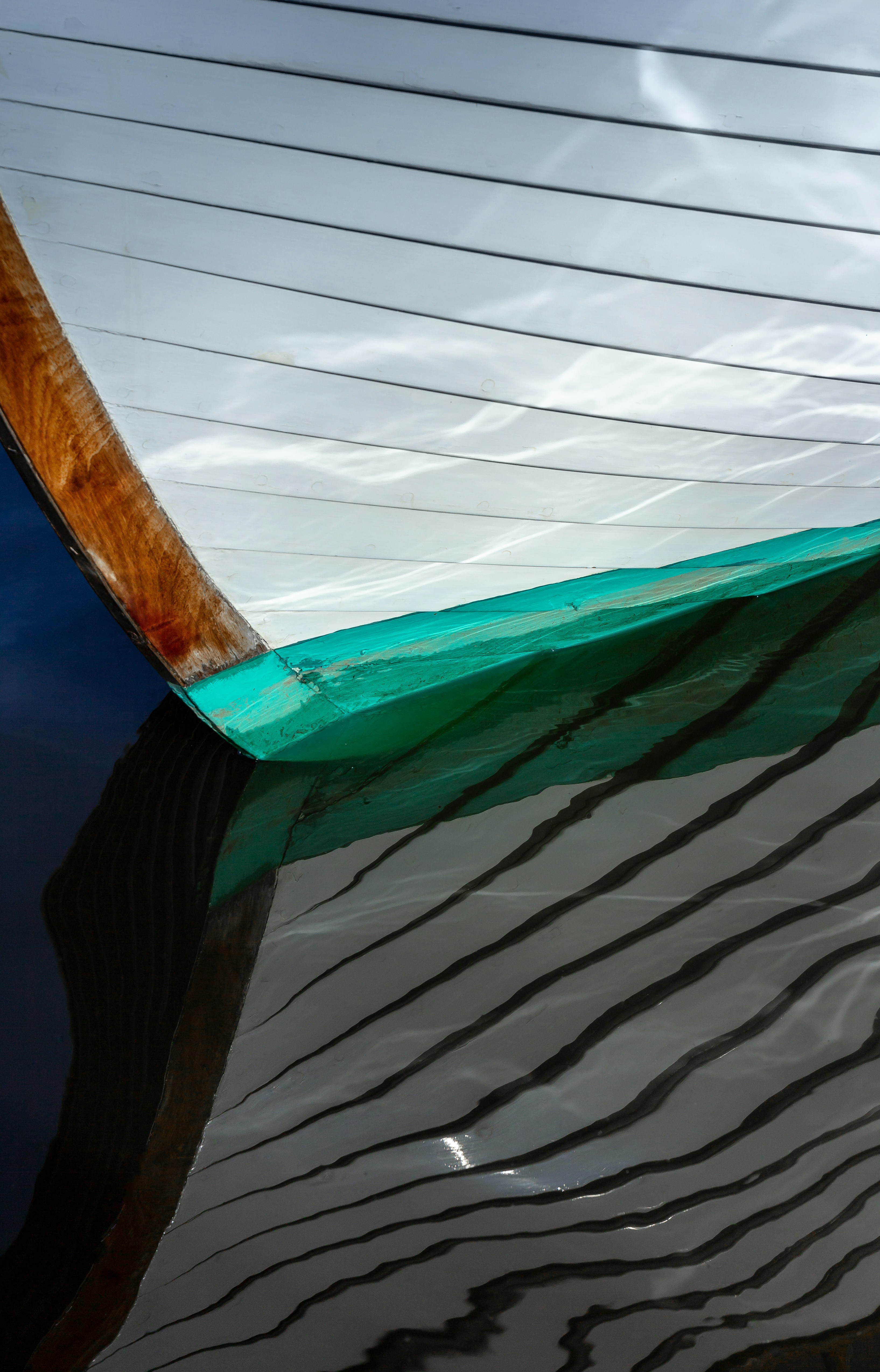 Curved bow of a boat reflecting in calm waters, showcasing a blend of colors and textures. The interplay of light and shadow enhances the visual appeal.