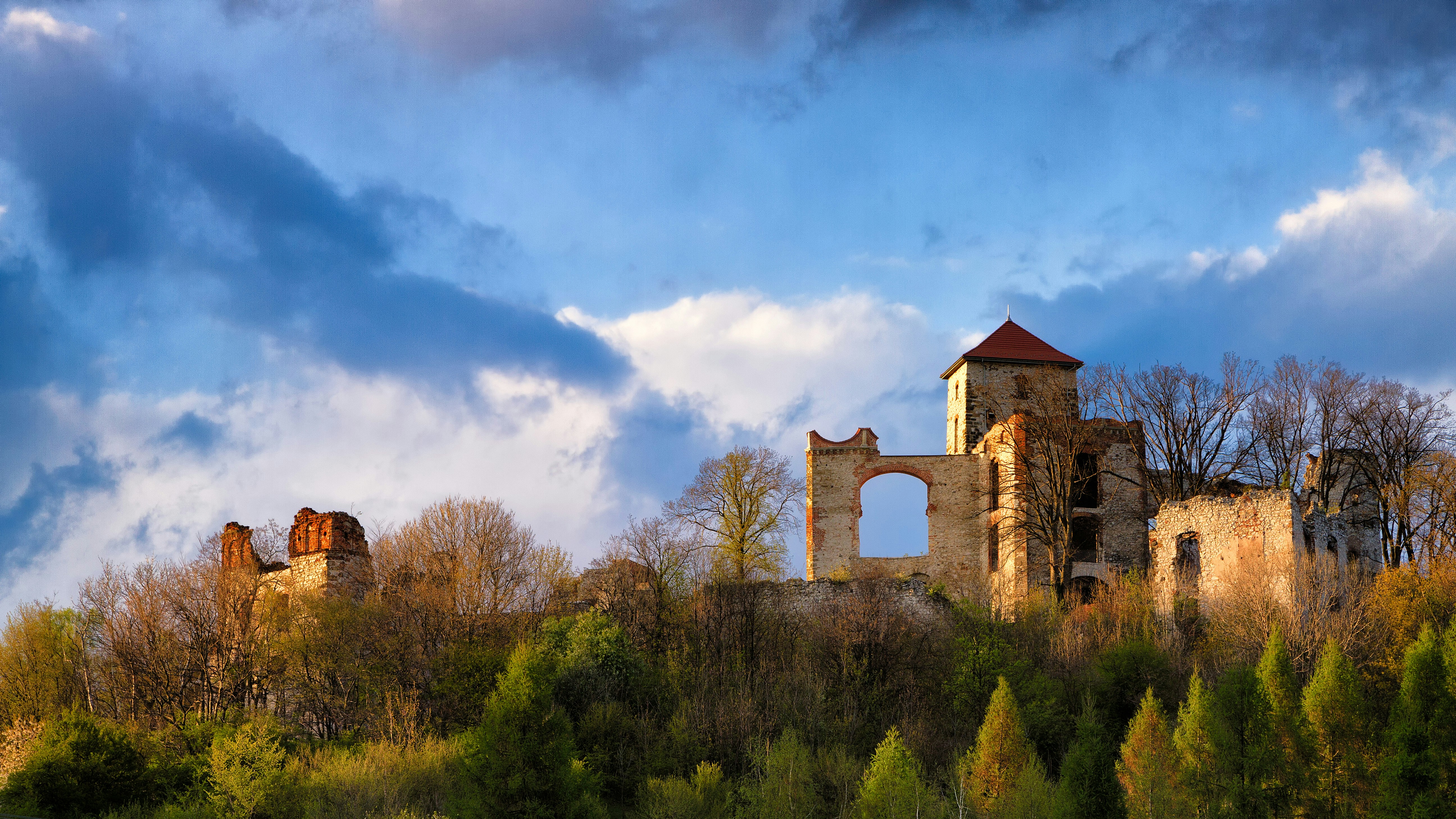 Ancient stone ruins perched on a hilltop, surrounded by lush trees under a dramatic sky.