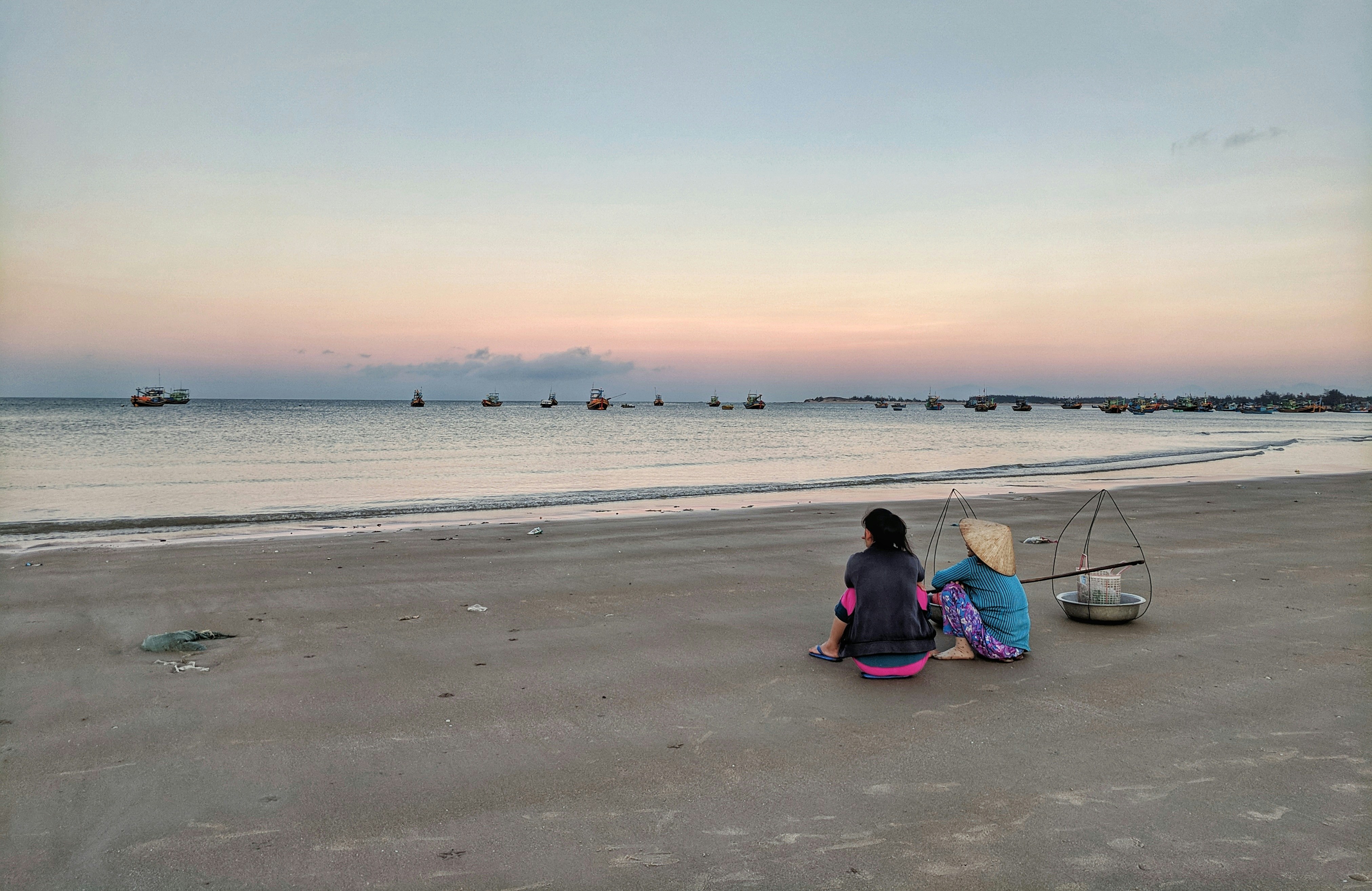 Evening by the Shore: Friends Rest on Wet Sand as Distant Boats Drift