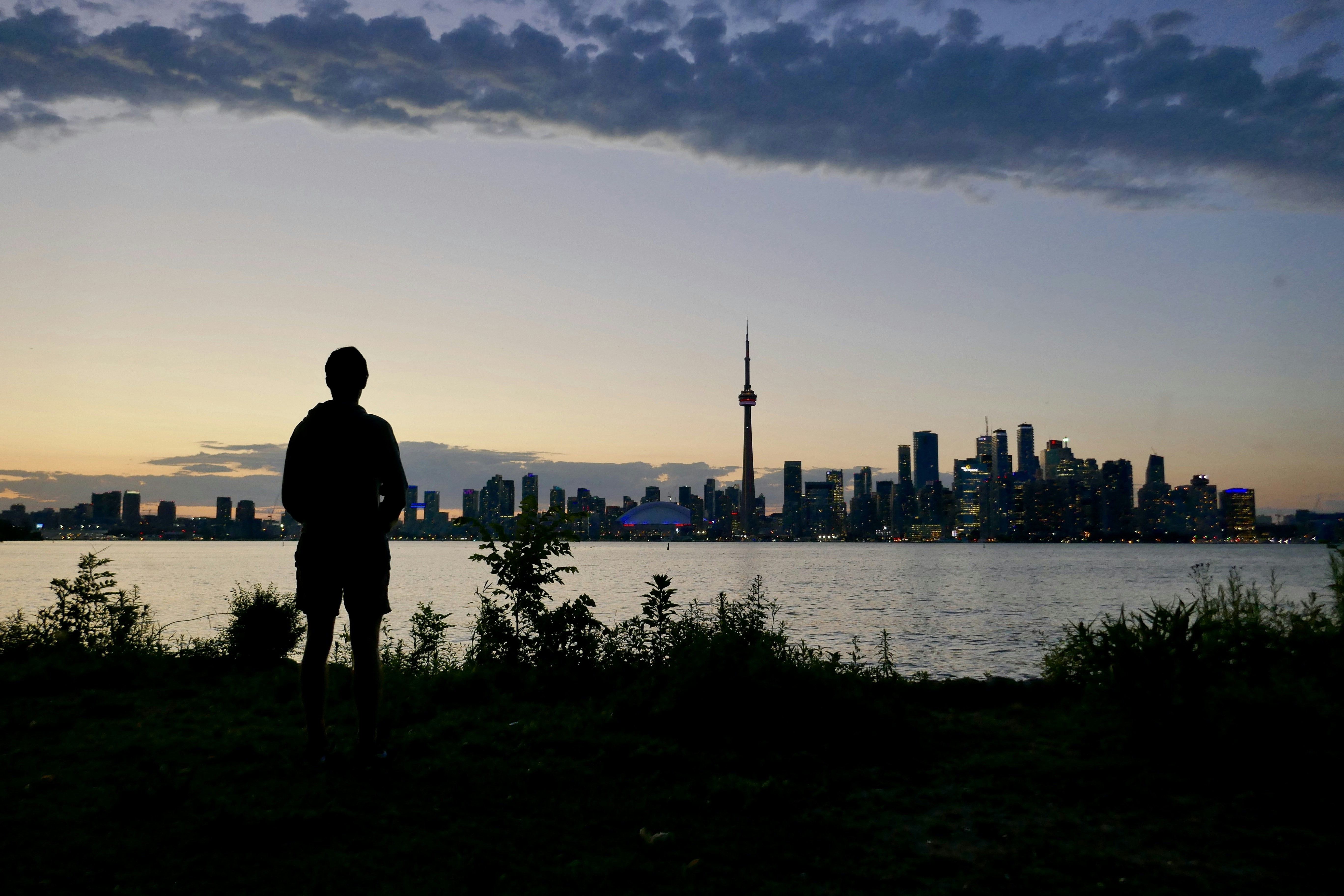 Silhouette of a person gazing at the Toronto skyline across Lake Ontario during twilight.