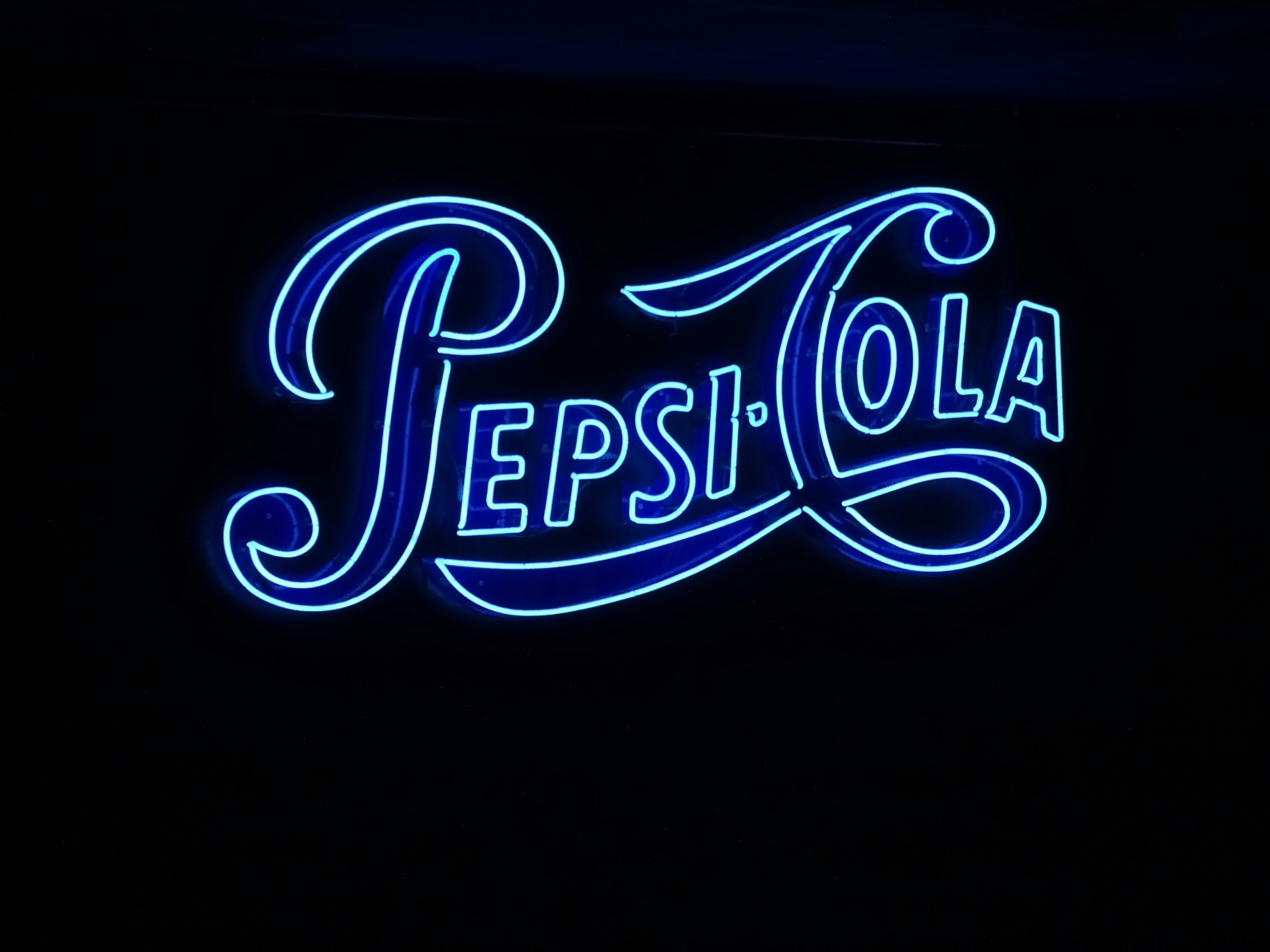 Illuminated Pepsi-Cola sign in vibrant blue neon against a dark background.