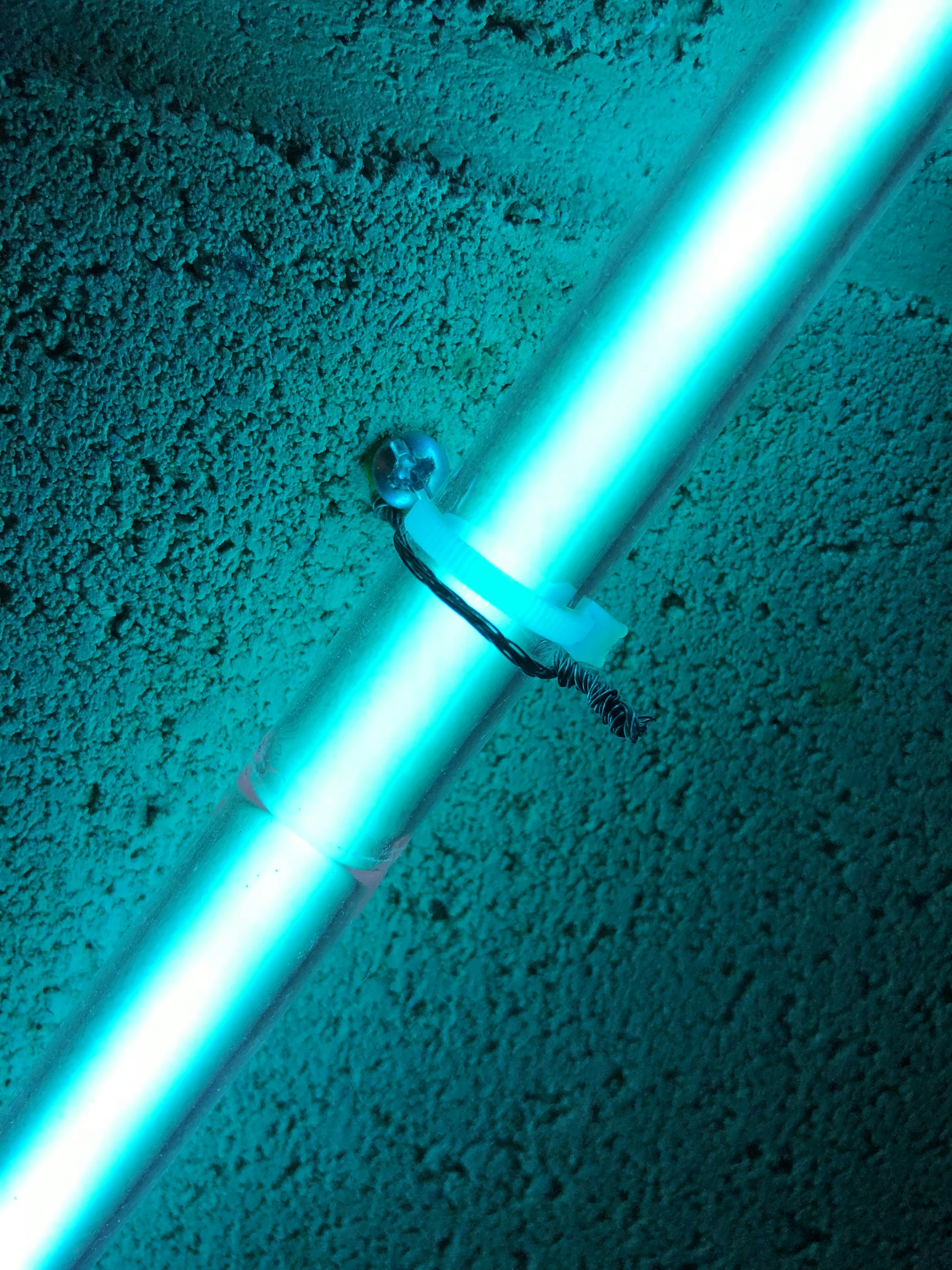 Cyan Neon Conduit: A Tangled Clamp on a Gritty Surface