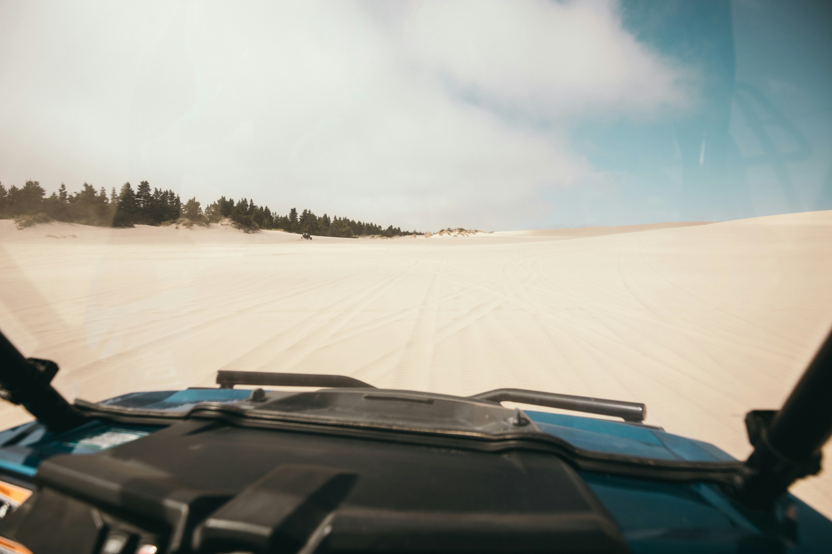 View from the driver's seat of an all-terrain vehicle navigating through expansive sand dunes under a partly cloudy sky.