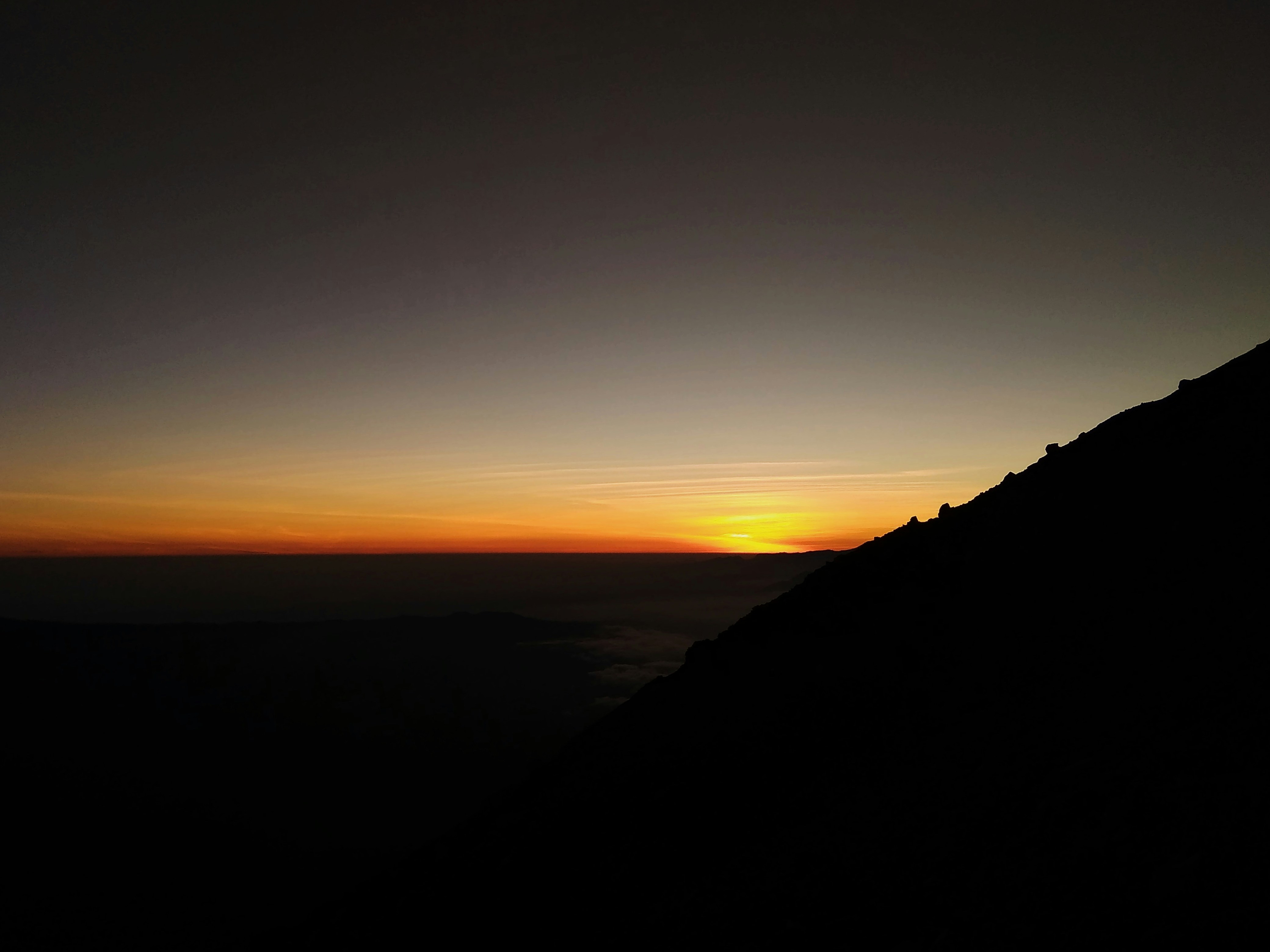 Sunset over a mountain ridge with a gradient sky transitioning from orange to deep blue.