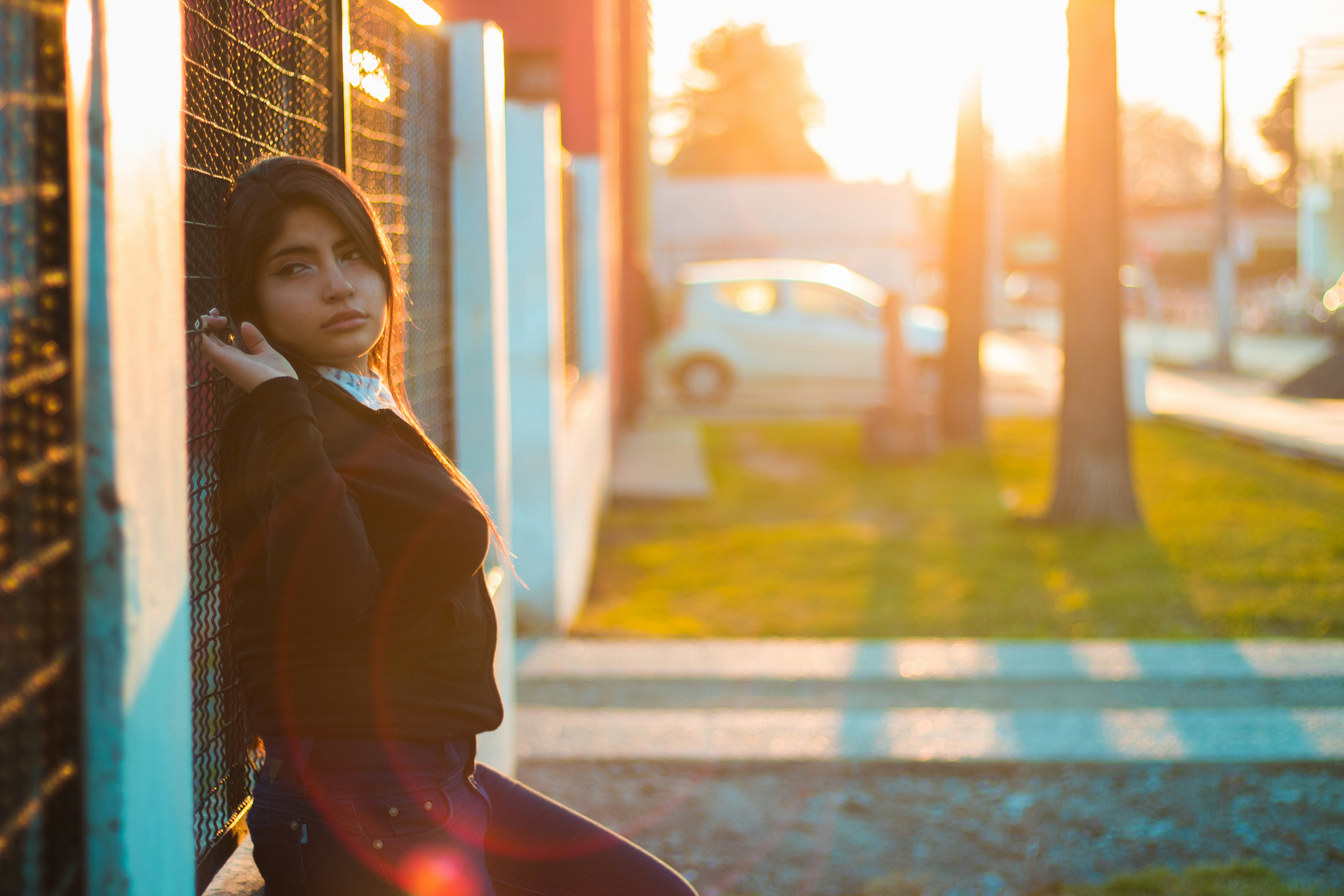 Person leaning against a fence in warm sunset light on a quiet street.
