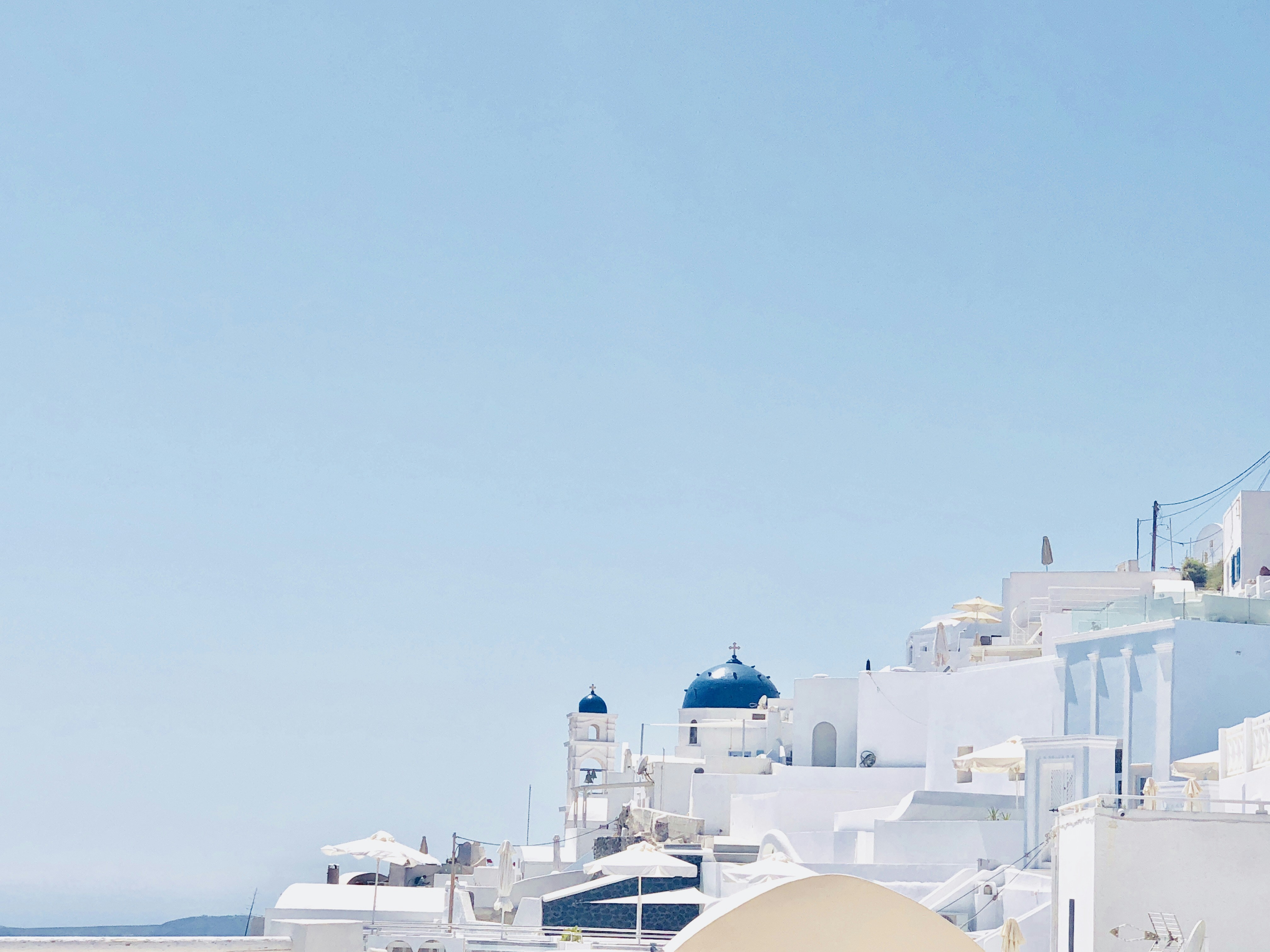 Whitewashed buildings with blue domes under a clear sky on a coastal hillside.