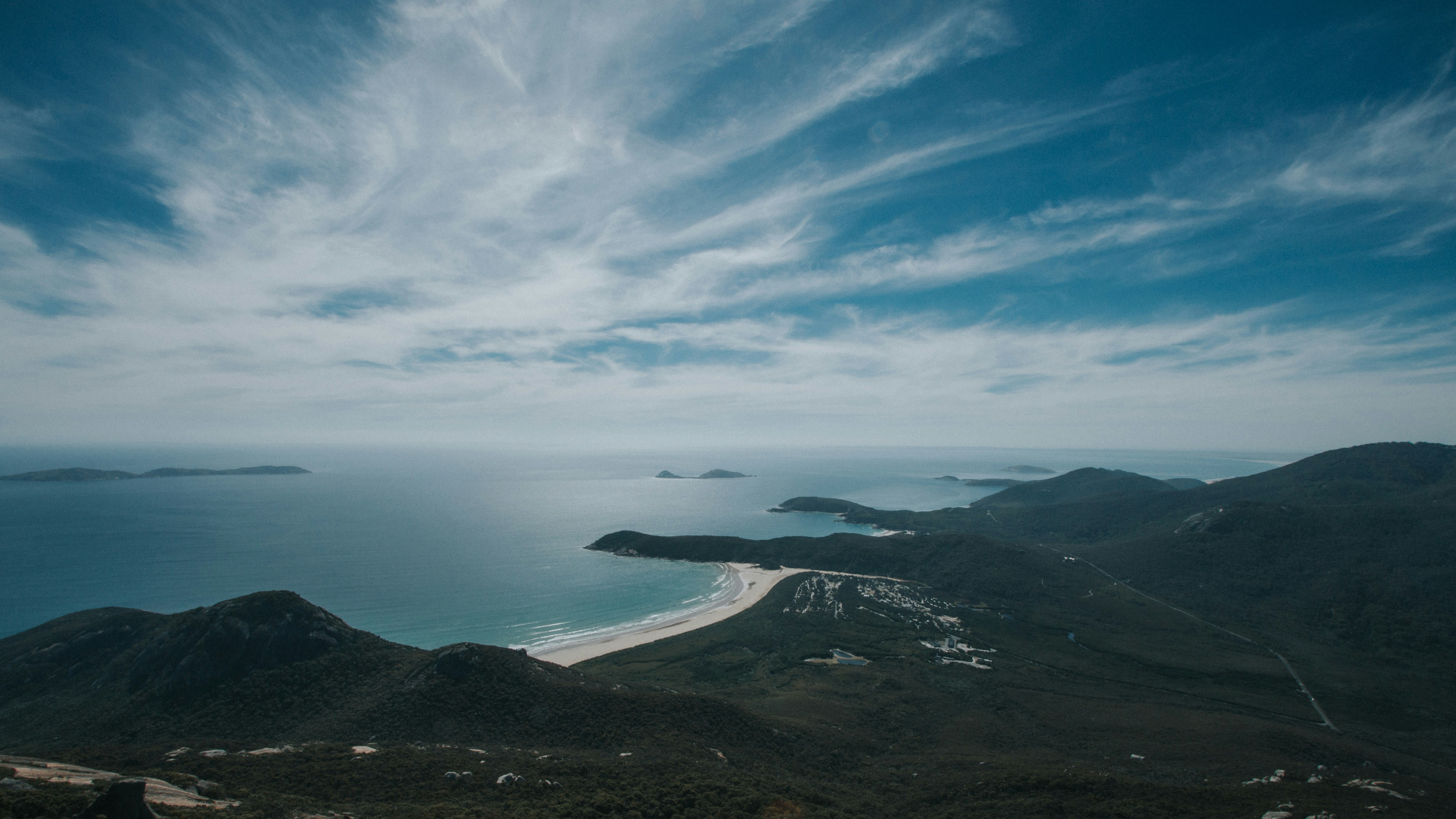 Expansive coastline with rolling hills meeting the ocean under a sky filled with wispy clouds.