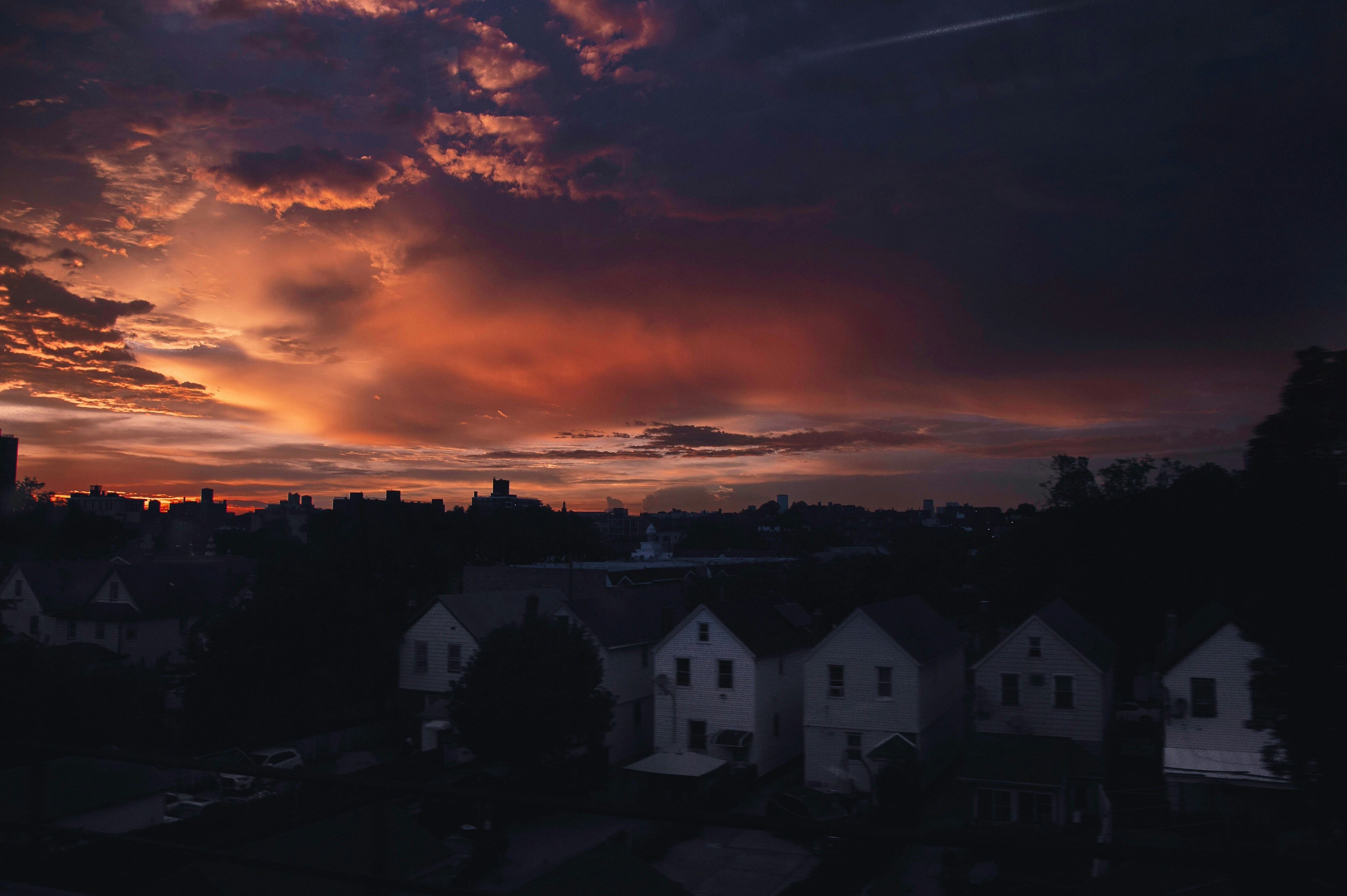 Vibrant sunset casting dramatic colors across a city skyline, silhouetting rooftops and clouds. The scene captures the transition from day to night.