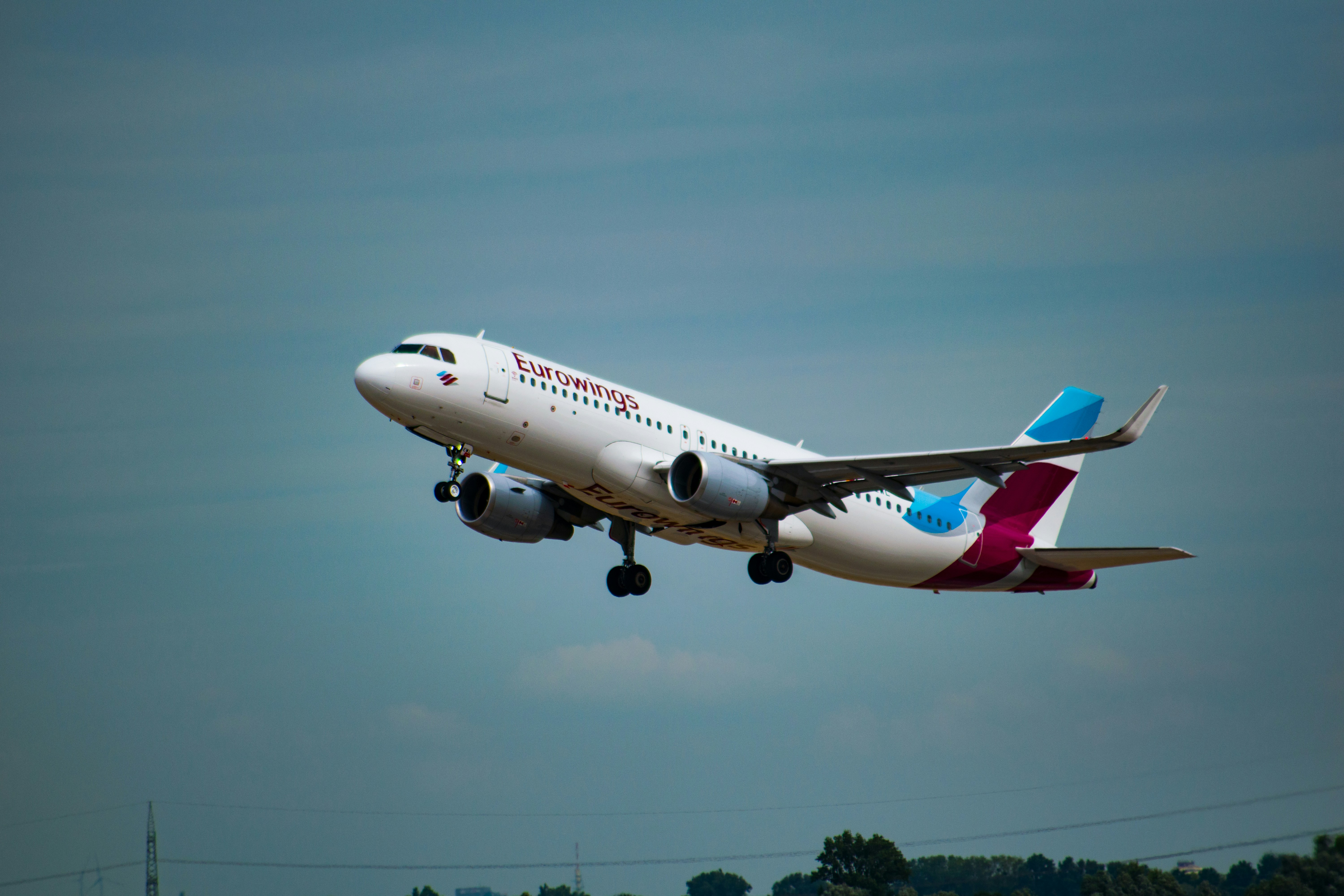 Airline aircraft ascending against a backdrop of blue skies and distant trees.