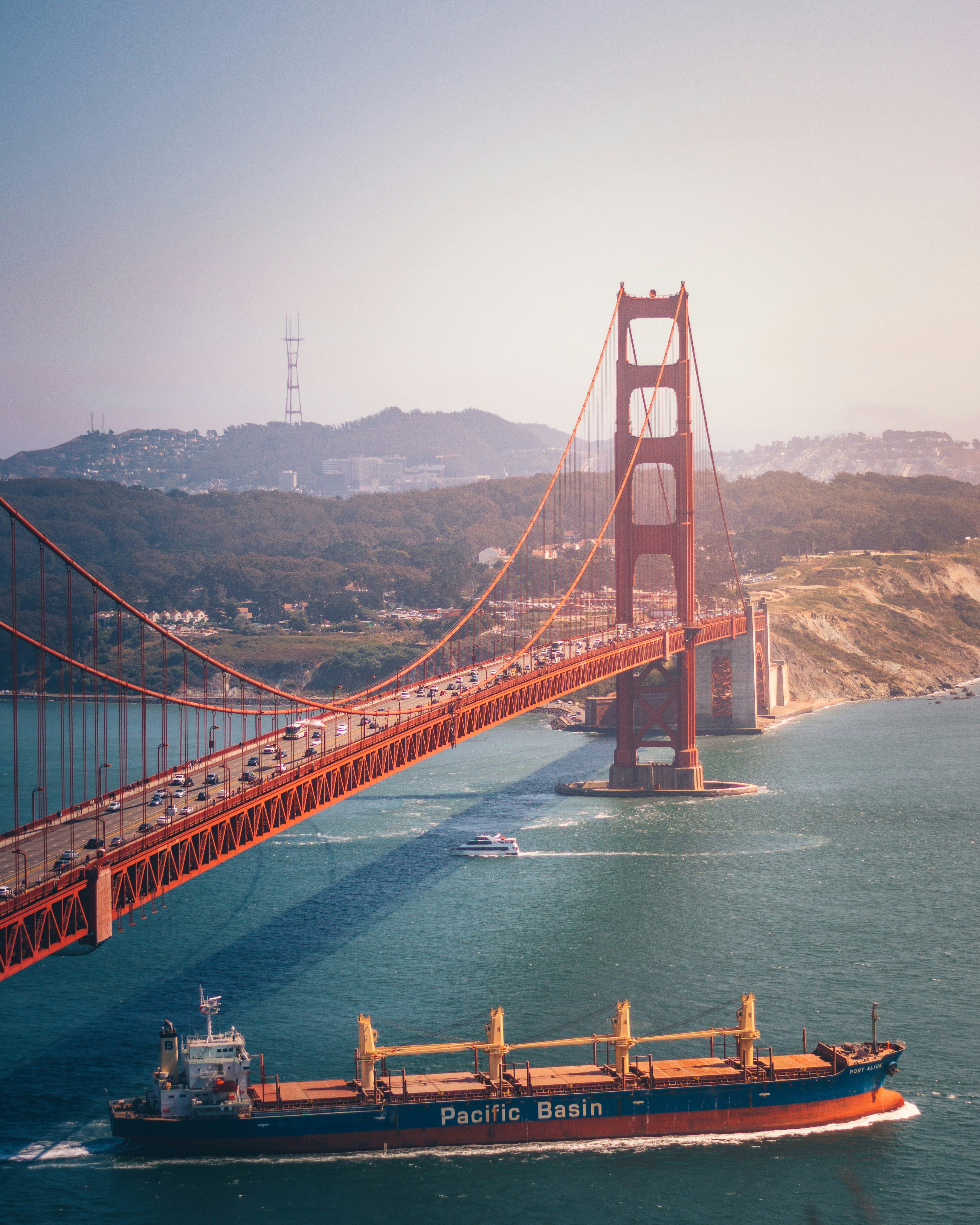 Golden Gate Bridge spanning across the bay, with a cargo ship navigating below and a scenic backdrop of hills. 