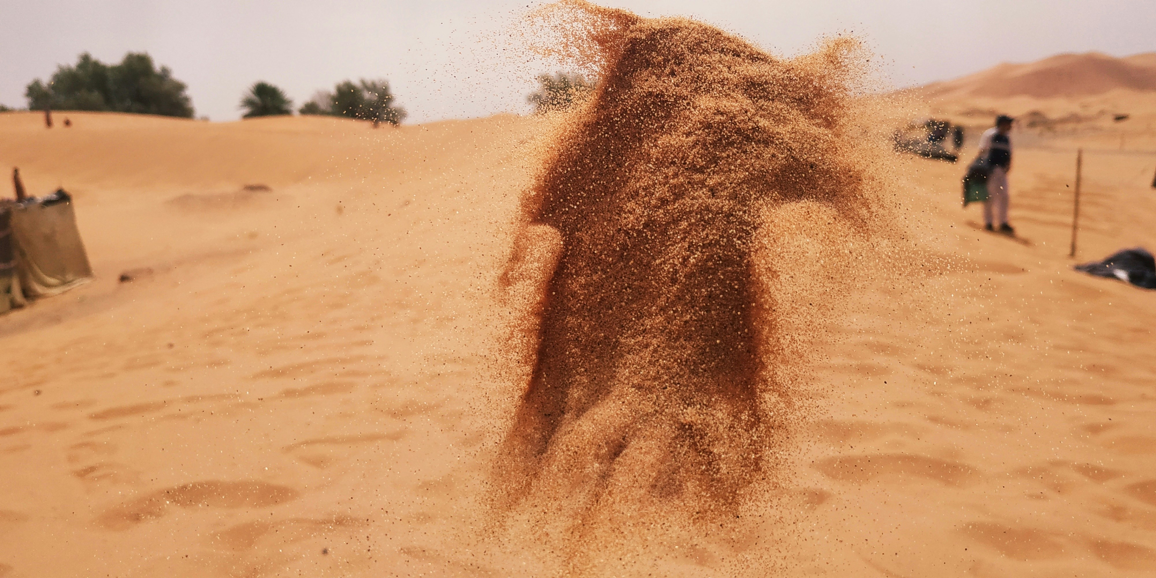 Sand bursts into the air against a backdrop of rolling desert dunes.