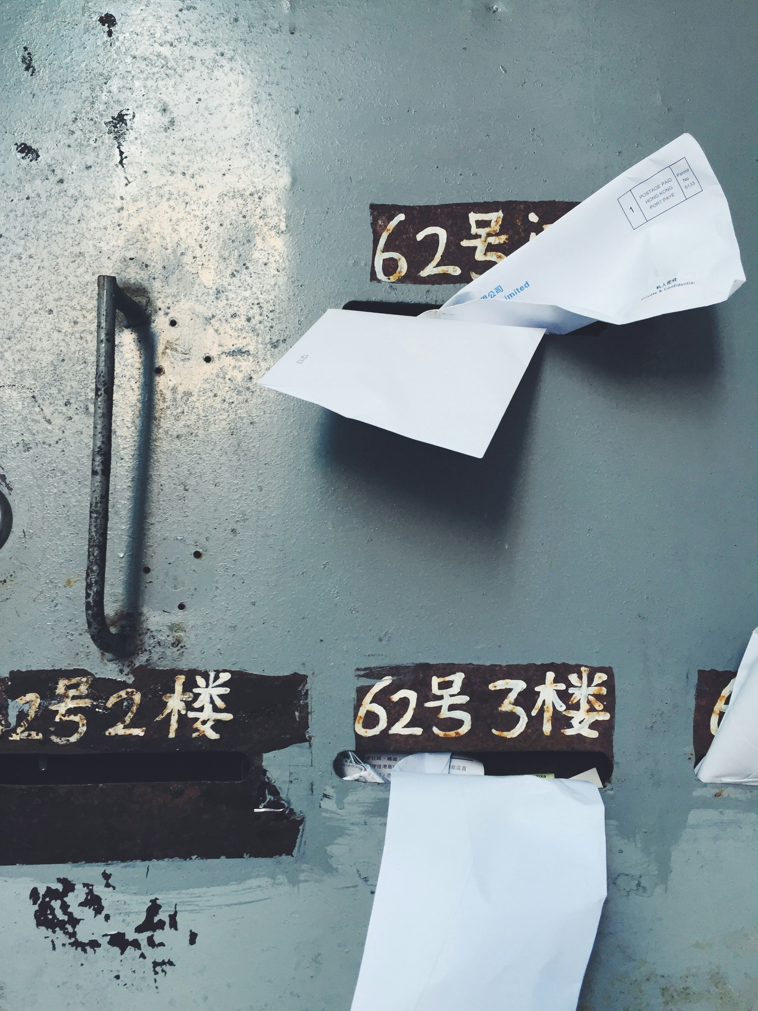 Dented white envelopes protruding from rustic mail slots on a weathered metal door.