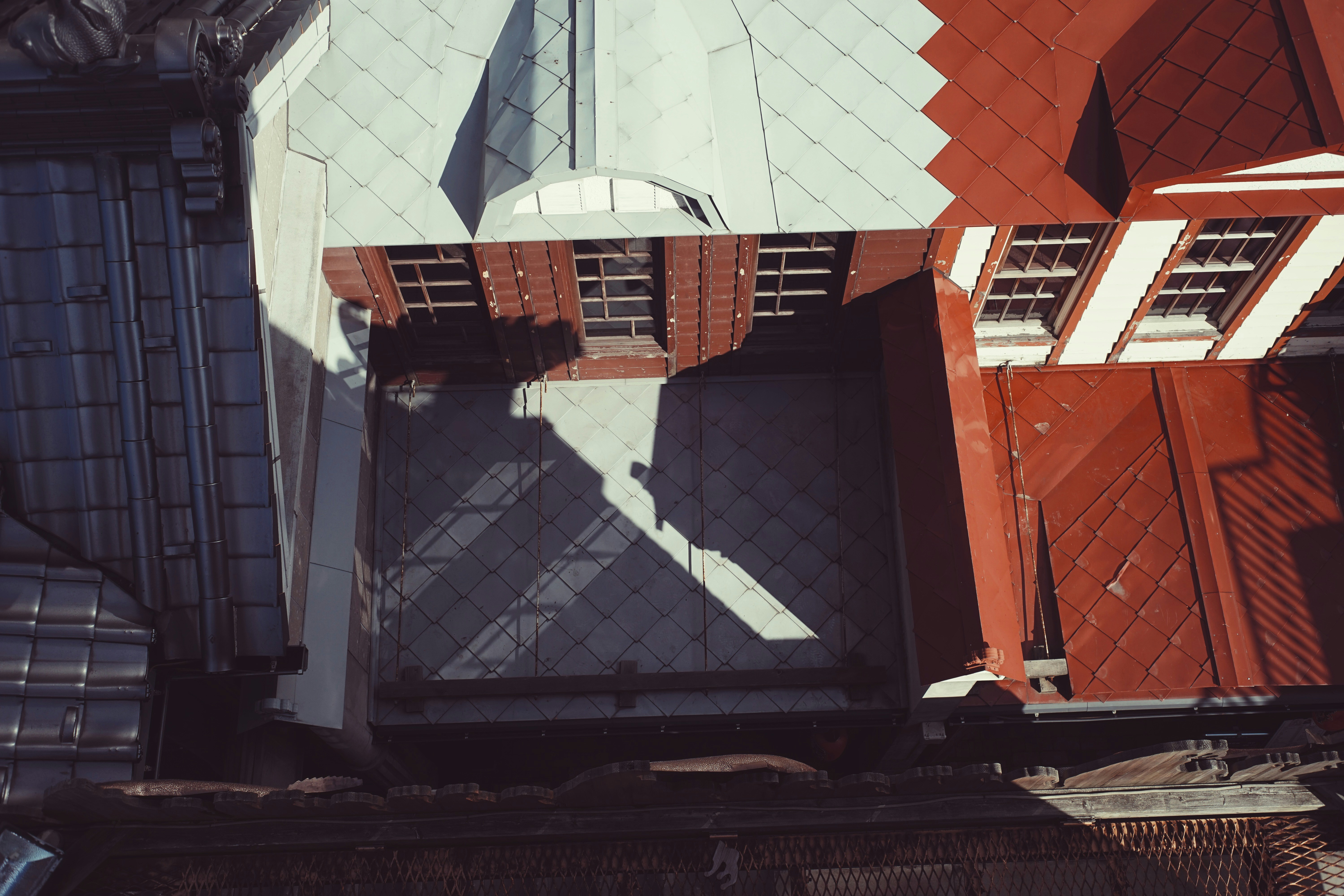 Overhead view of a courtyard surrounded by buildings, showcasing intricate roof patterns and shadows cast by midday sun.