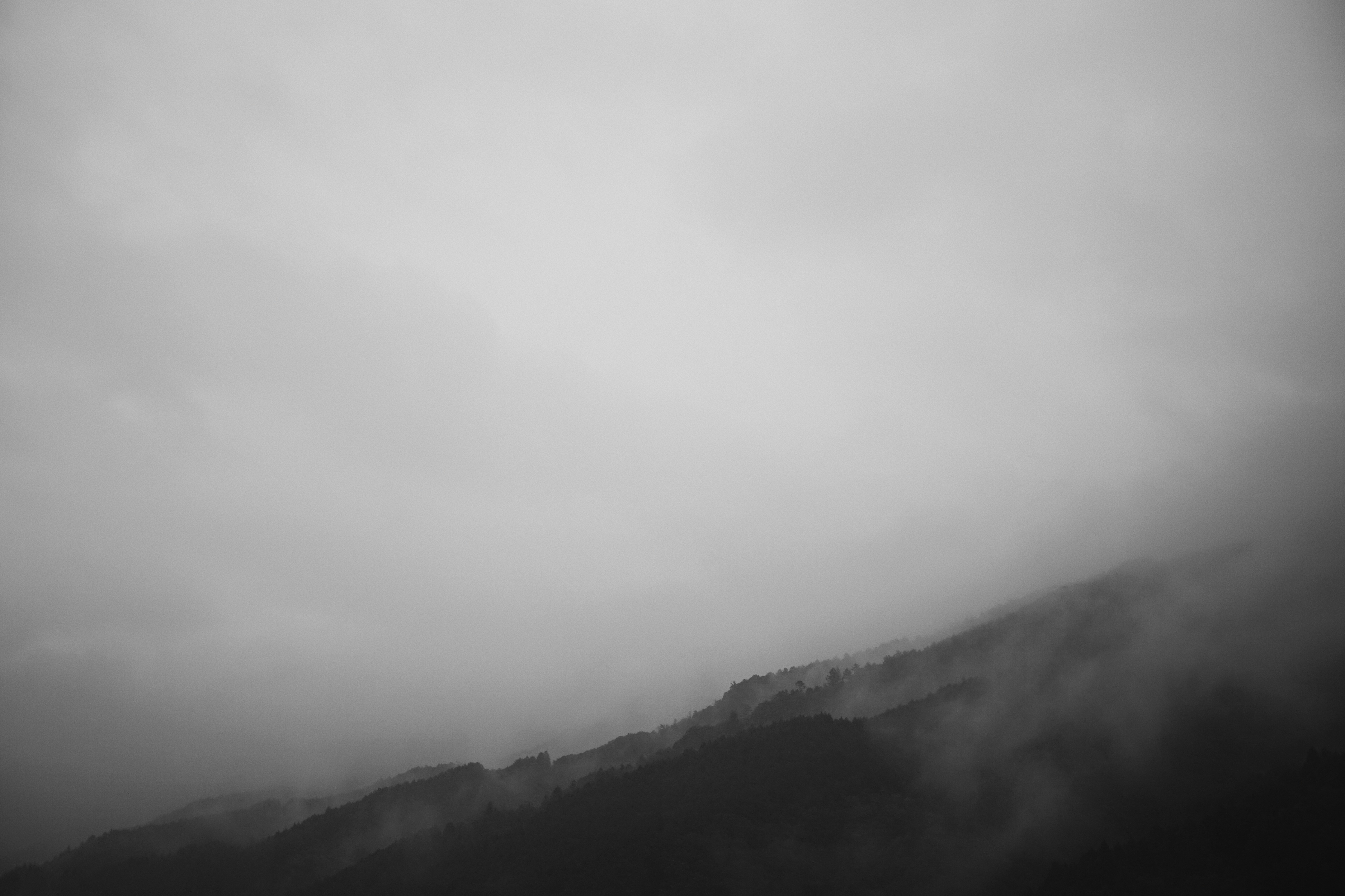Misty mountains partially obscured by dense fog under a gray sky.