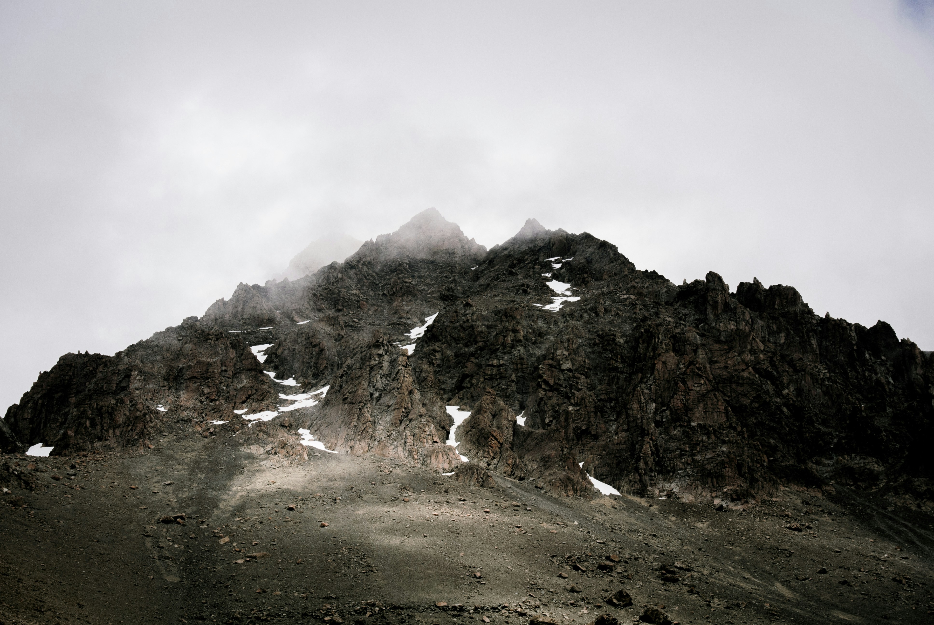 Rocky mountain peaks shrouded in mist with patches of snow under an overcast sky.