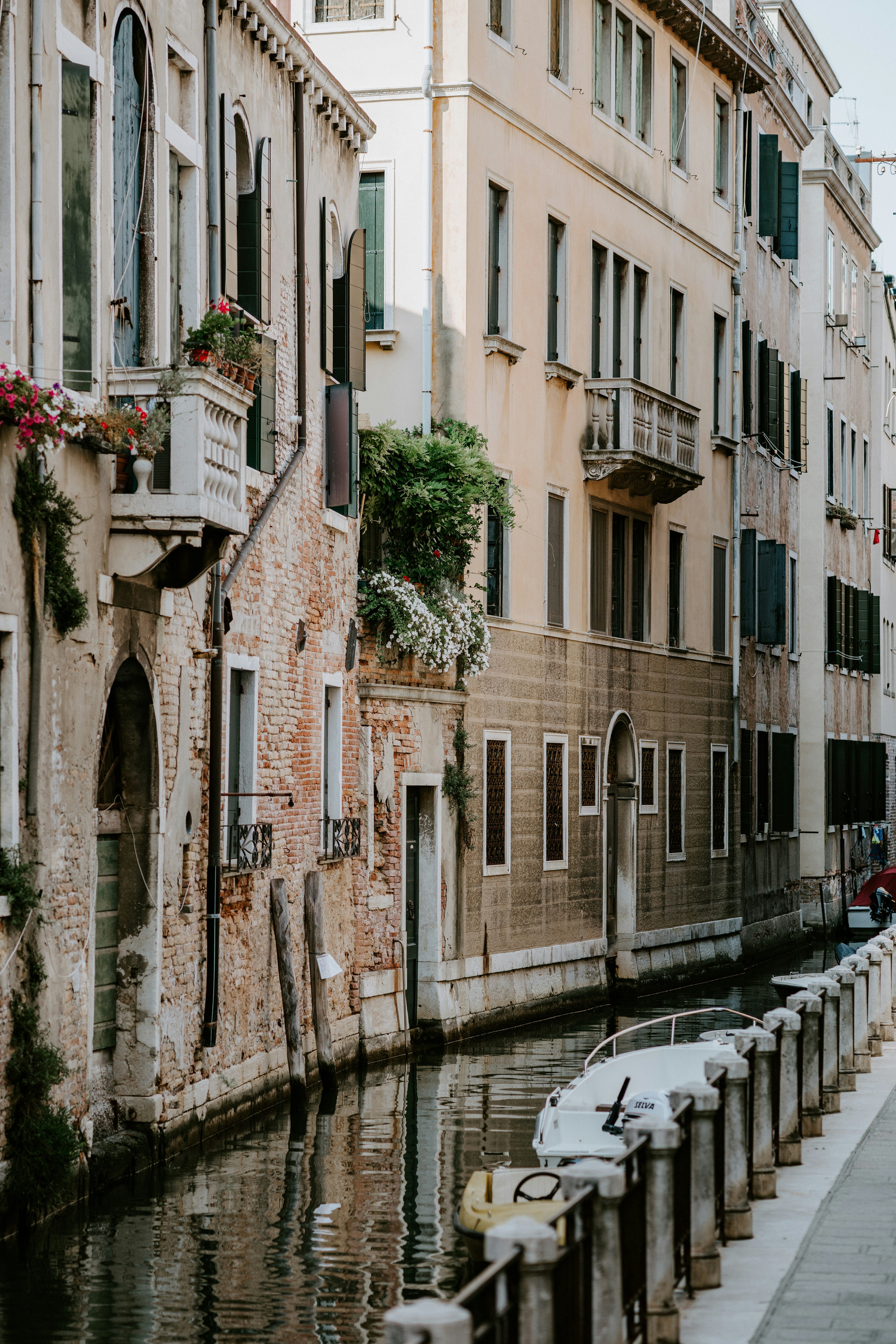 Charming canal lined with historic buildings and blooming flowers, reflecting the essence of Venetian architecture and tranquility.