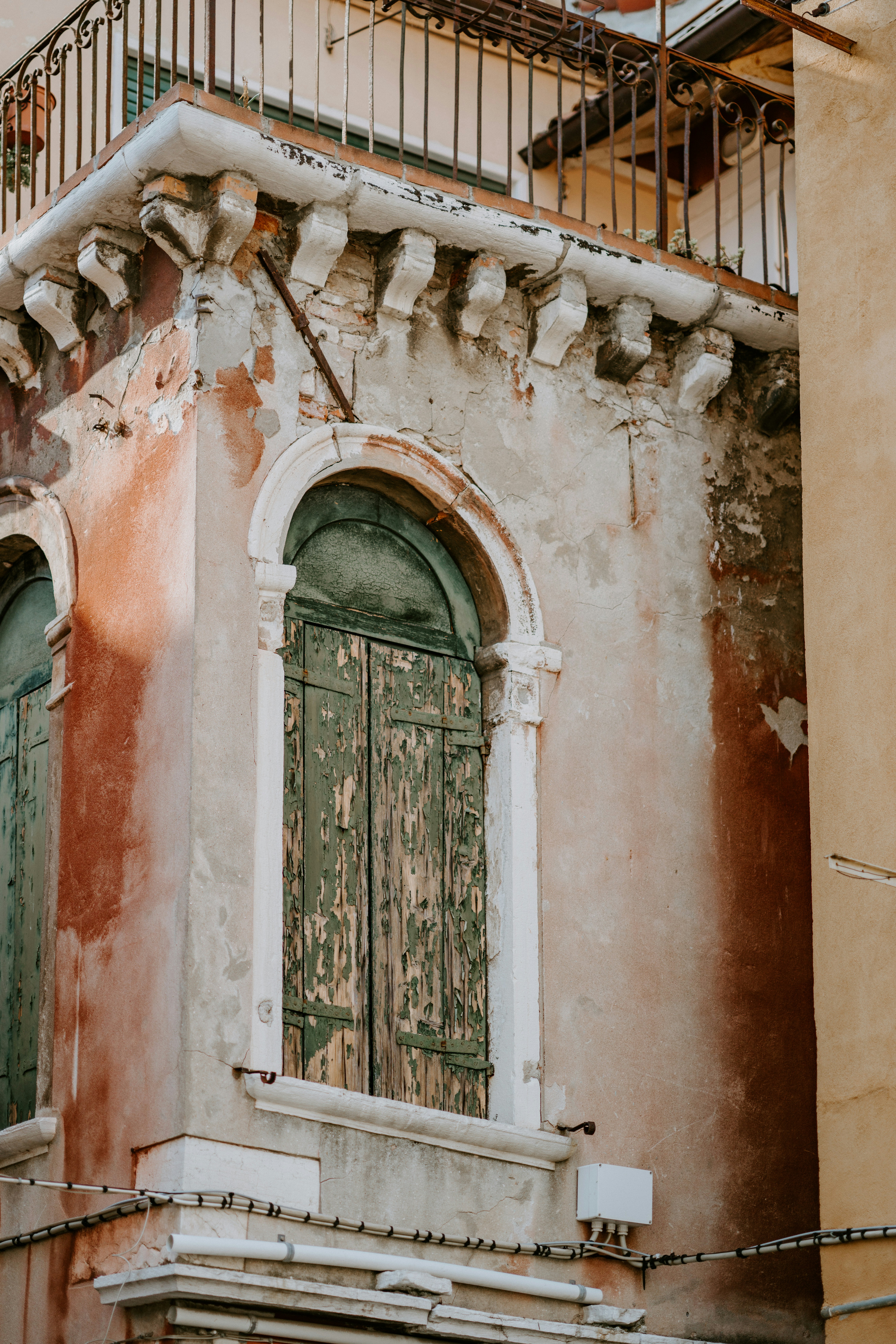 A weathered building corner featuring peeling green shutters and textured walls, reflecting a rich history. The architectural details hint at a bygone era.