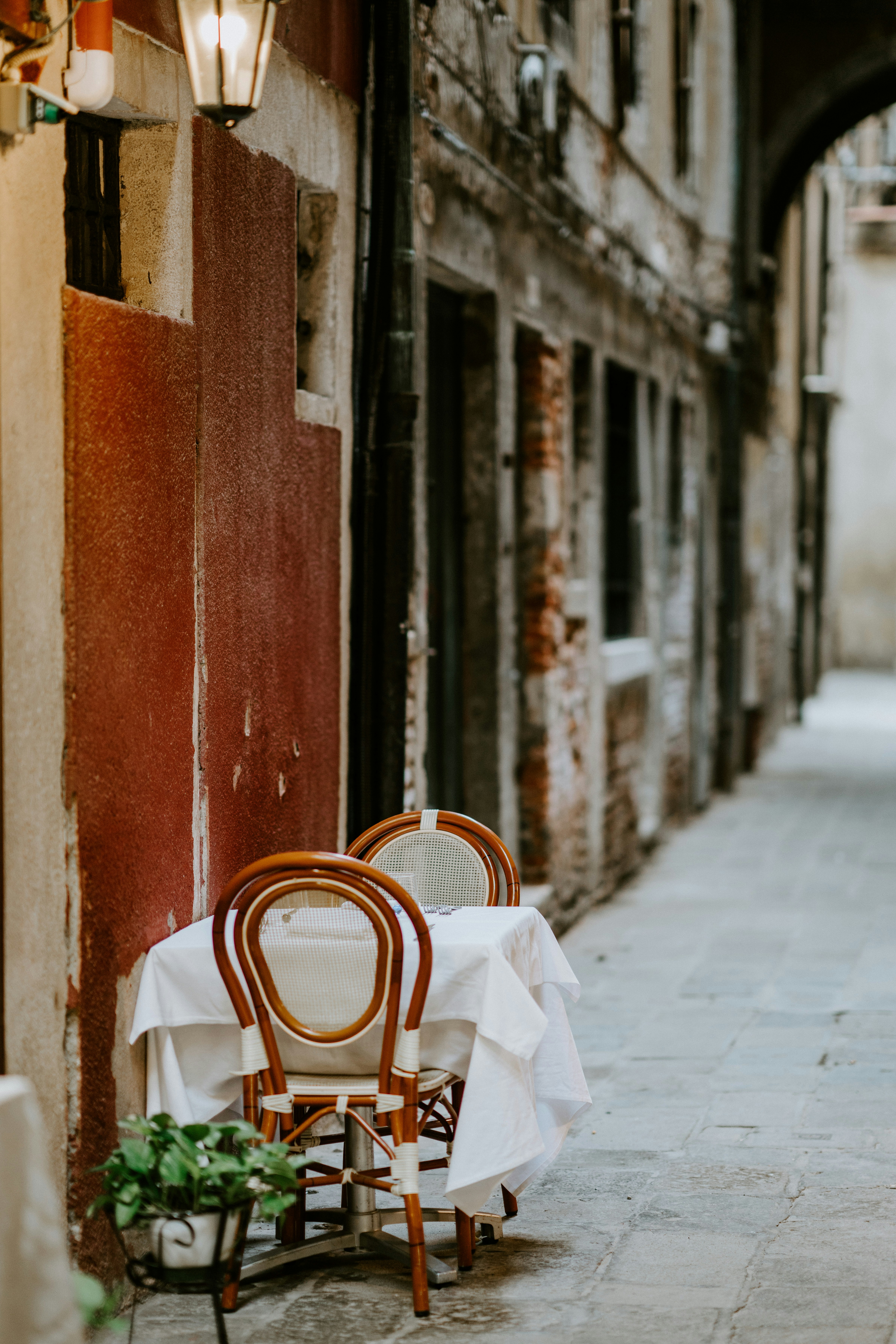 Charming outdoor dining setup with wooden chairs and a white tablecloth nestled in a quaint alleyway, framed by rustic walls and soft lighting.