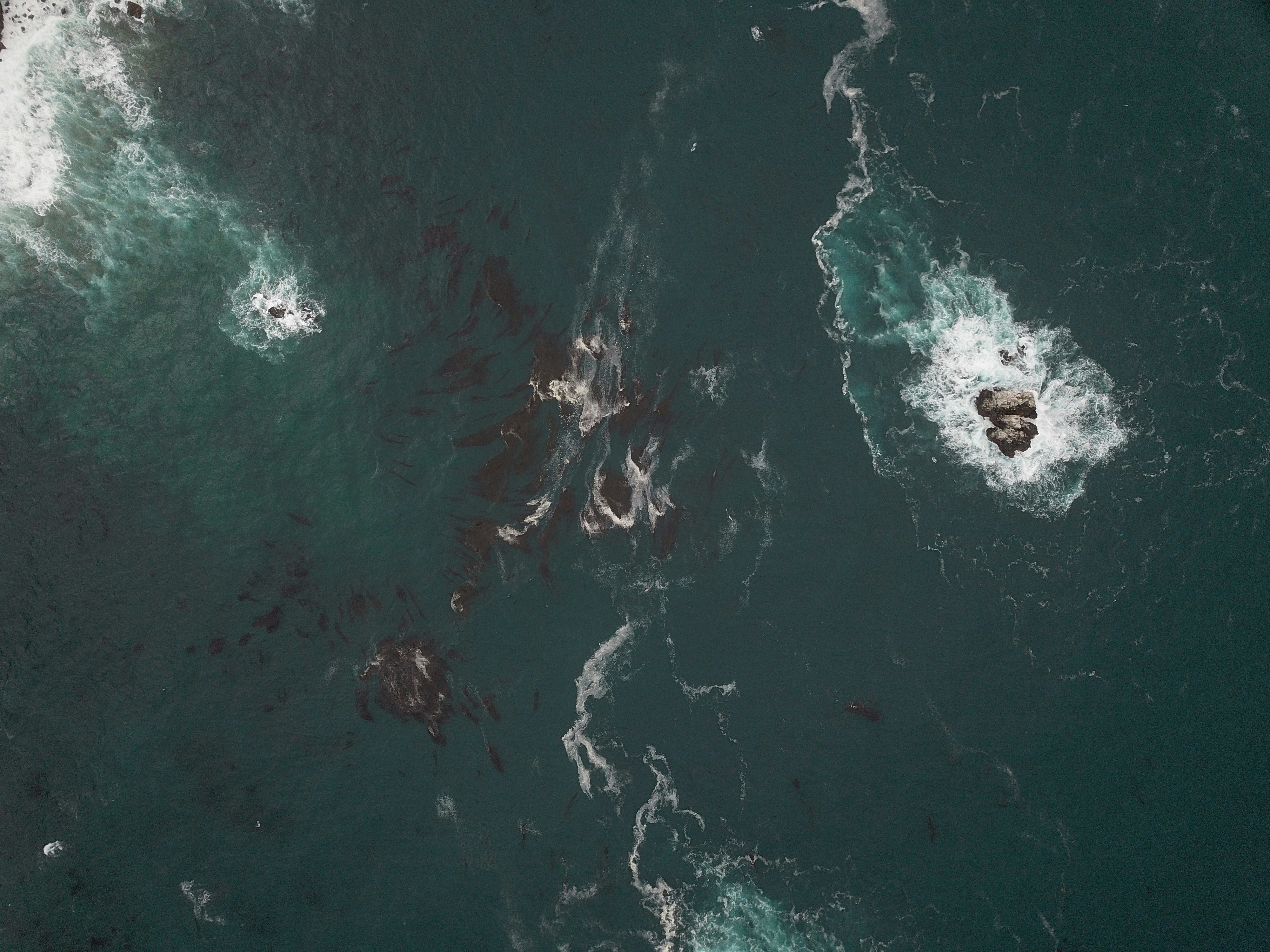 Aerial view of ocean waves forming a face-like pattern with rocks and surf.