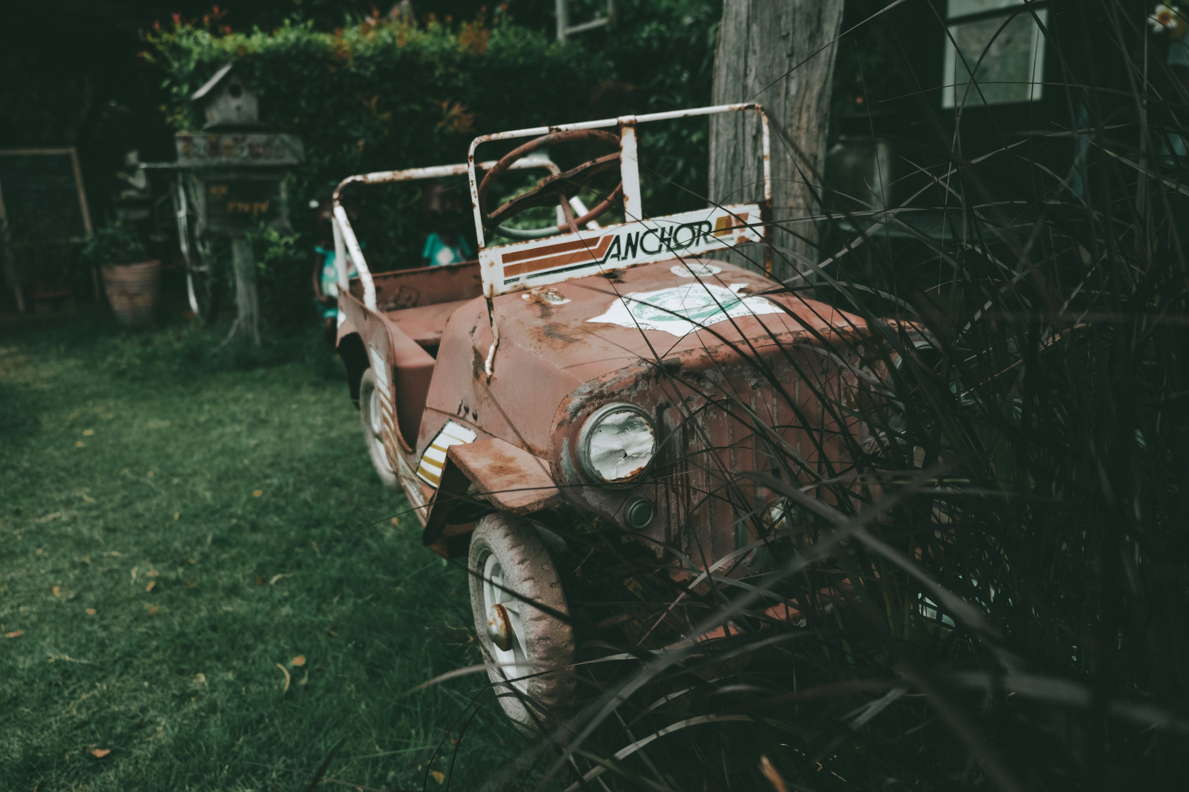 Vintage jeep partially hidden by overgrown grass, with a sign reading 'ANCHOR' on the front. The scene evokes nostalgia and a sense of forgotten journeys.