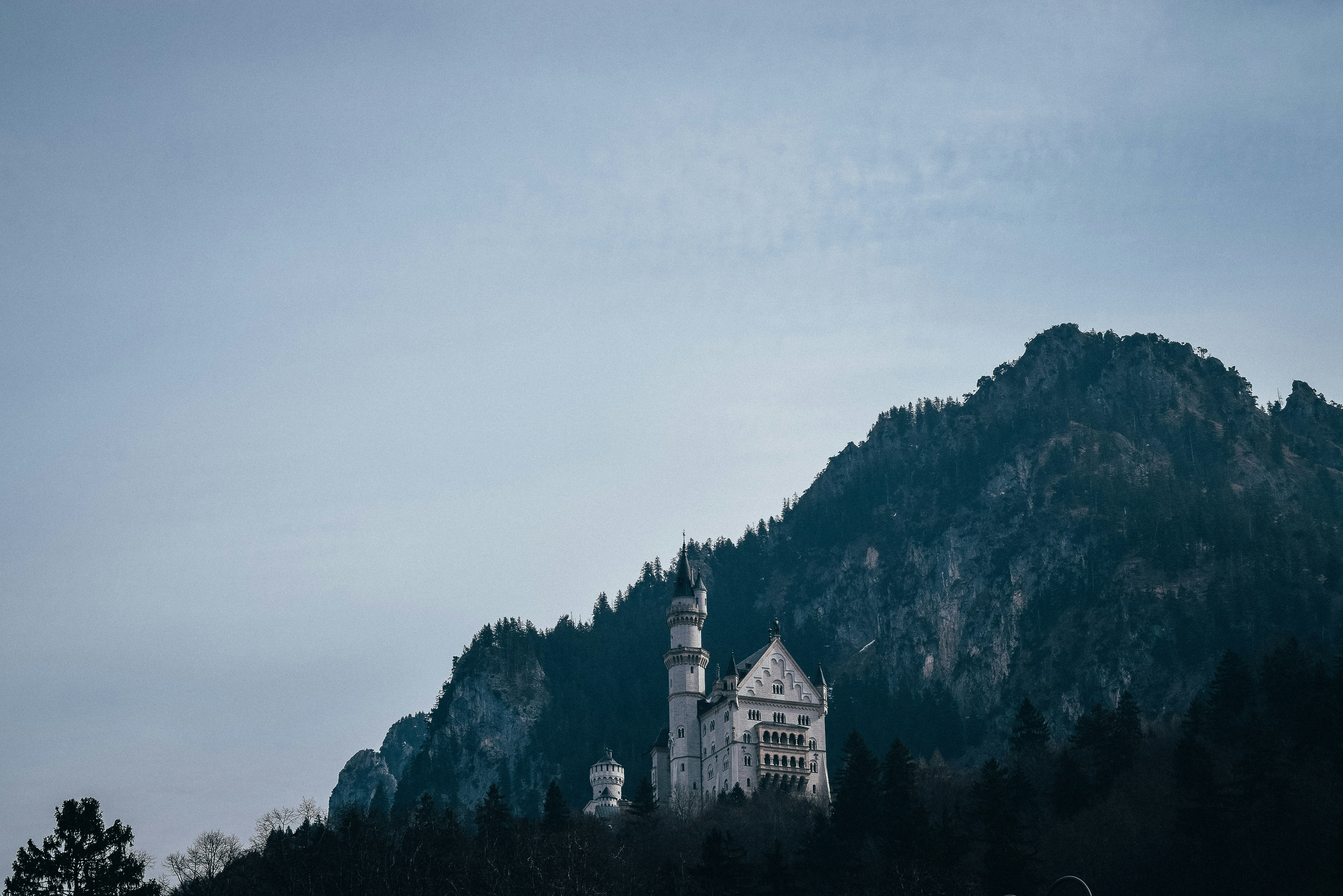 A majestic castle perched against a rugged mountain backdrop, shrouded in a serene atmosphere. The scene evokes a sense of mystery and timeless beauty.