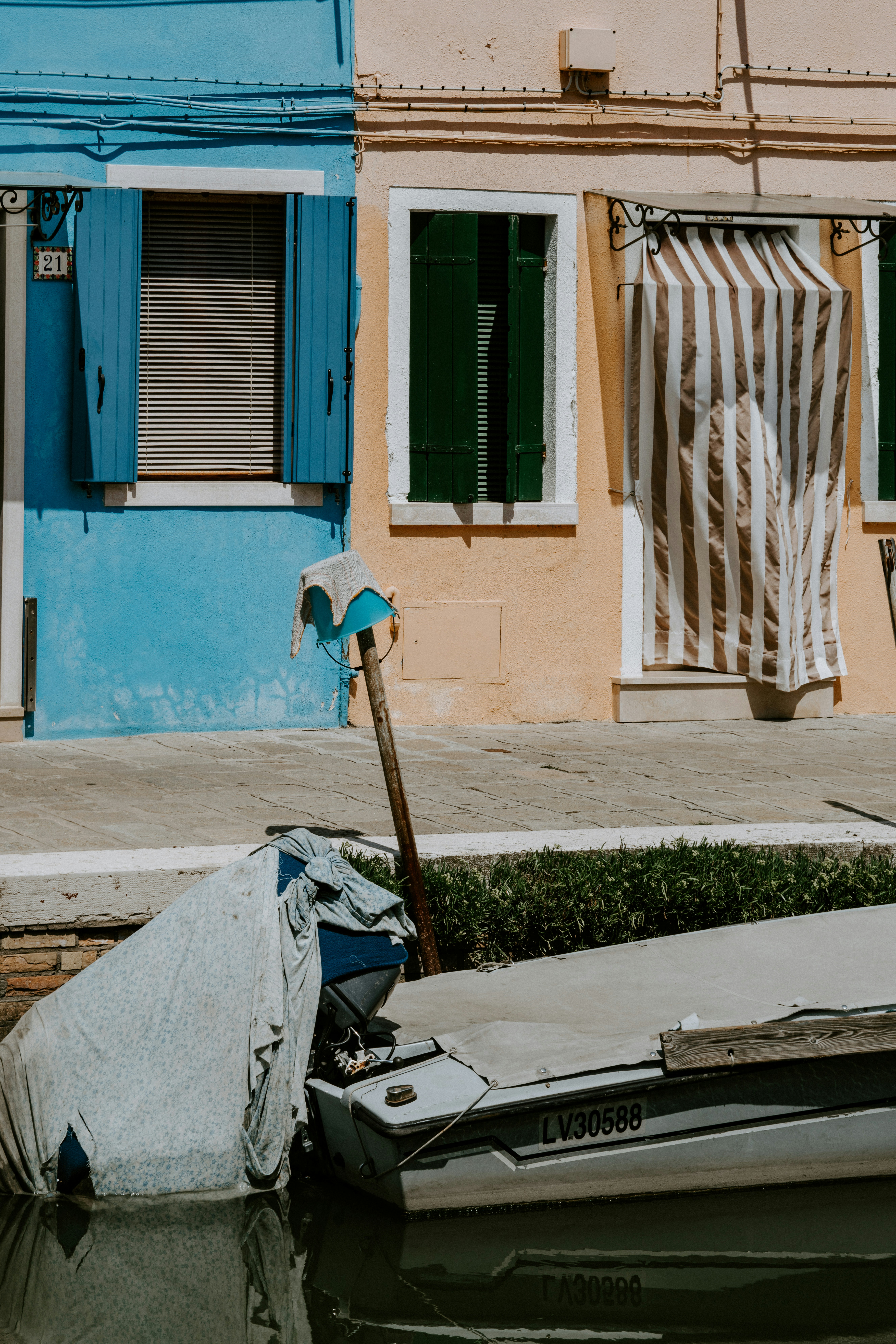 Colorful houses line the canal, with a partially covered boat resting quietly. Striped curtains flutter gently in the breeze.