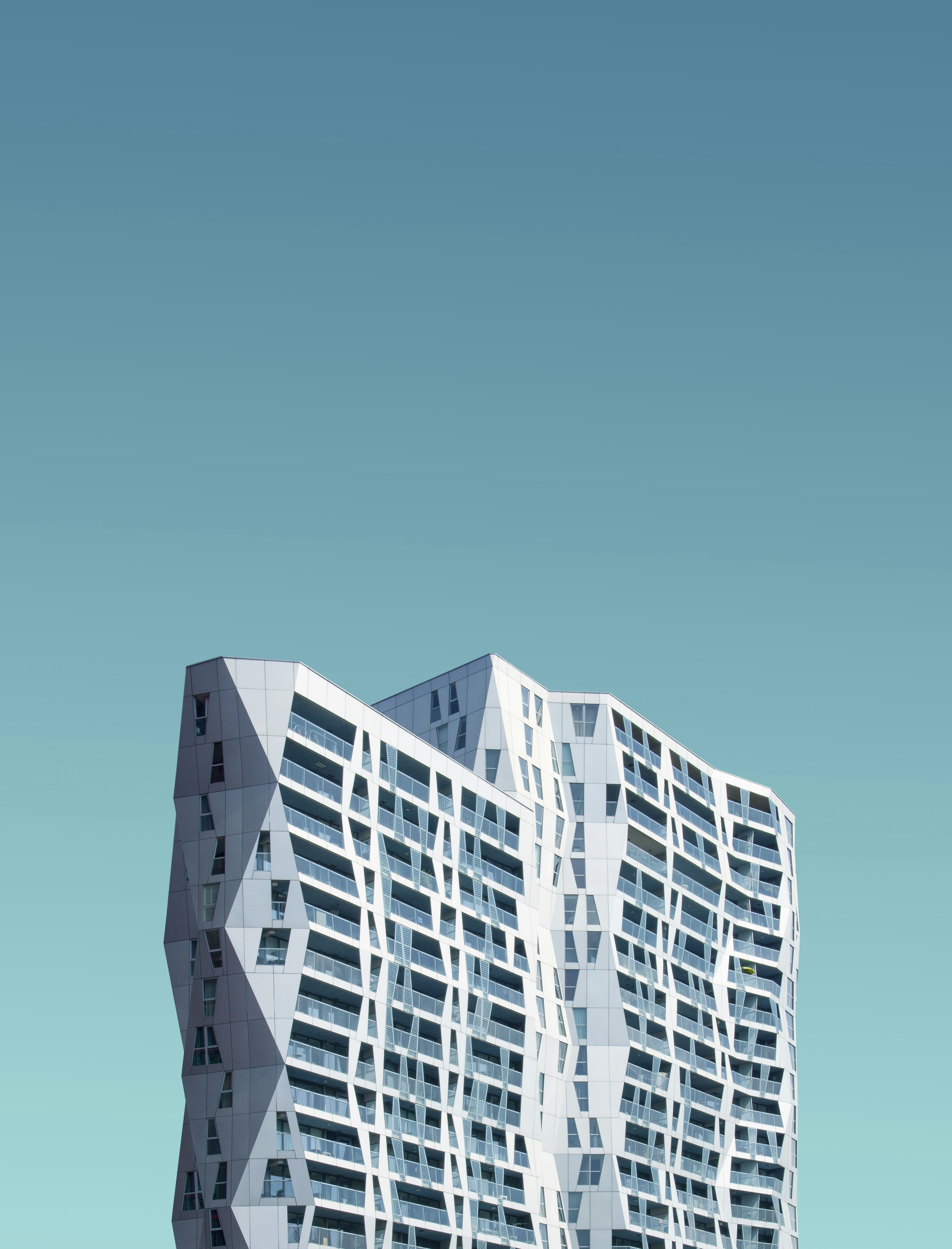 Abstract architectural design of a building featuring angular shapes and reflective glass panels against a clear sky.