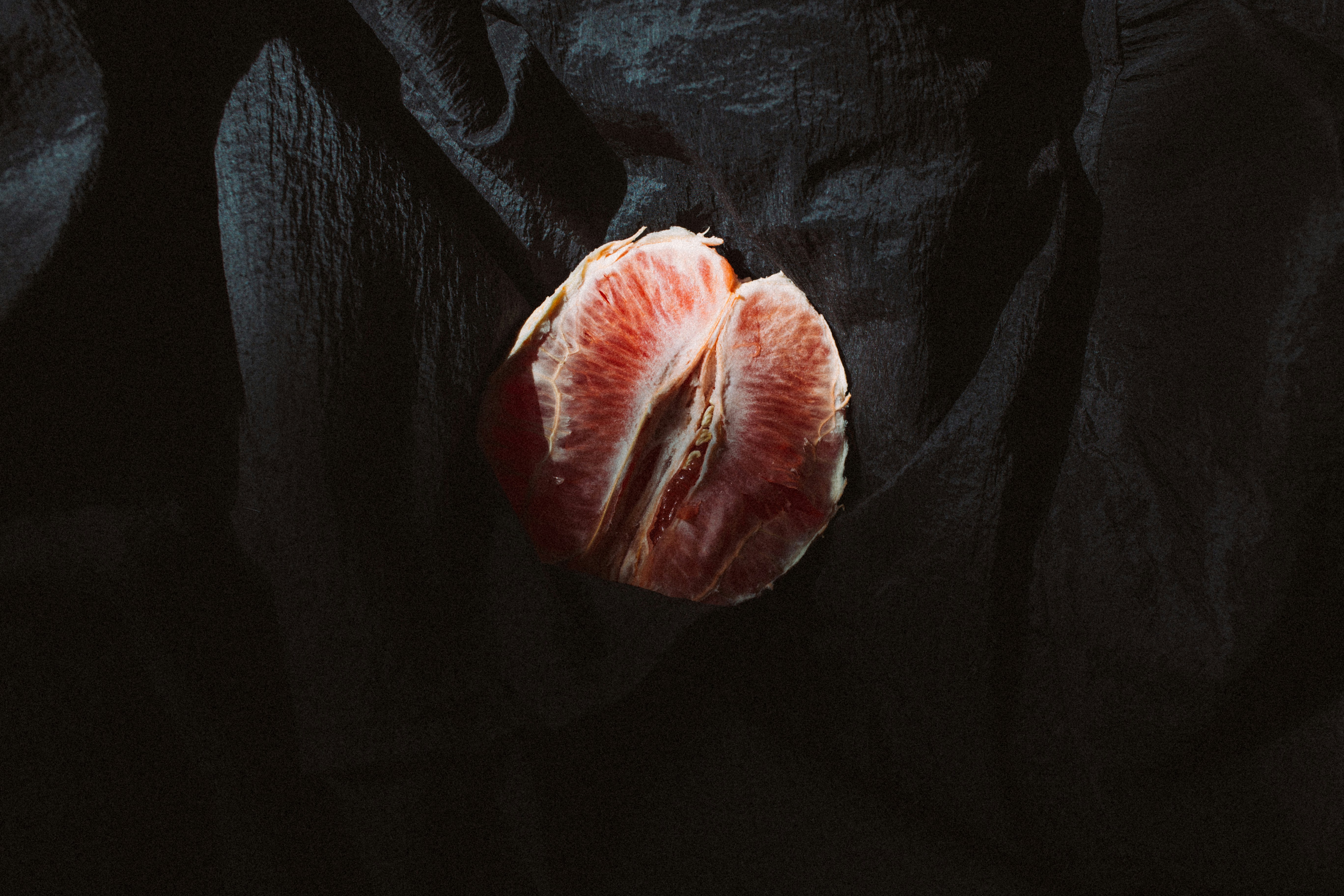 Halved grapefruit resting on textured dark fabric, showcasing vibrant pink and white segments.