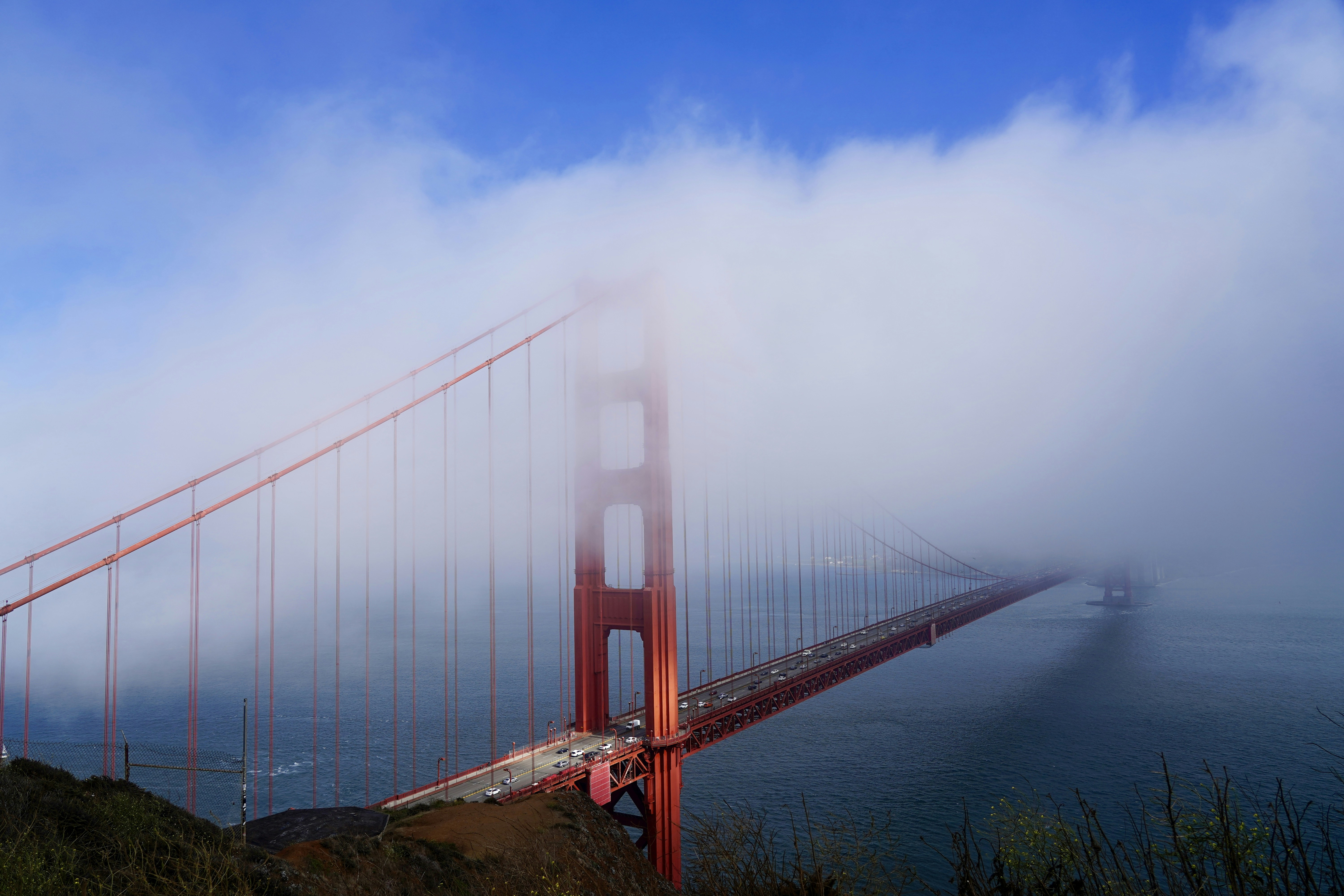 Iconic red bridge partially shrouded in coastal fog under a vibrant blue sky.