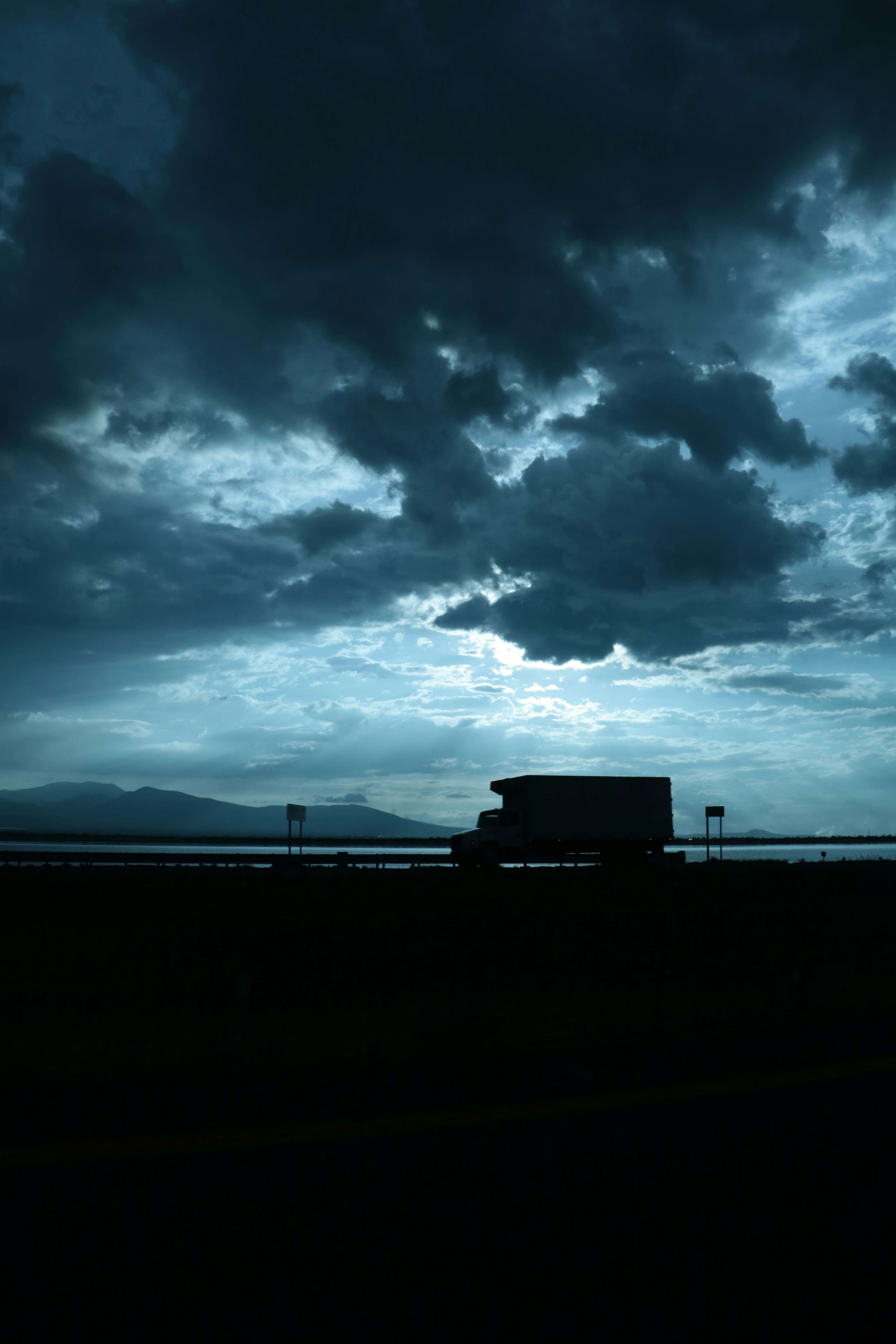 Silhouette of a truck against a moody sky, with dramatic clouds and fading light in the background.