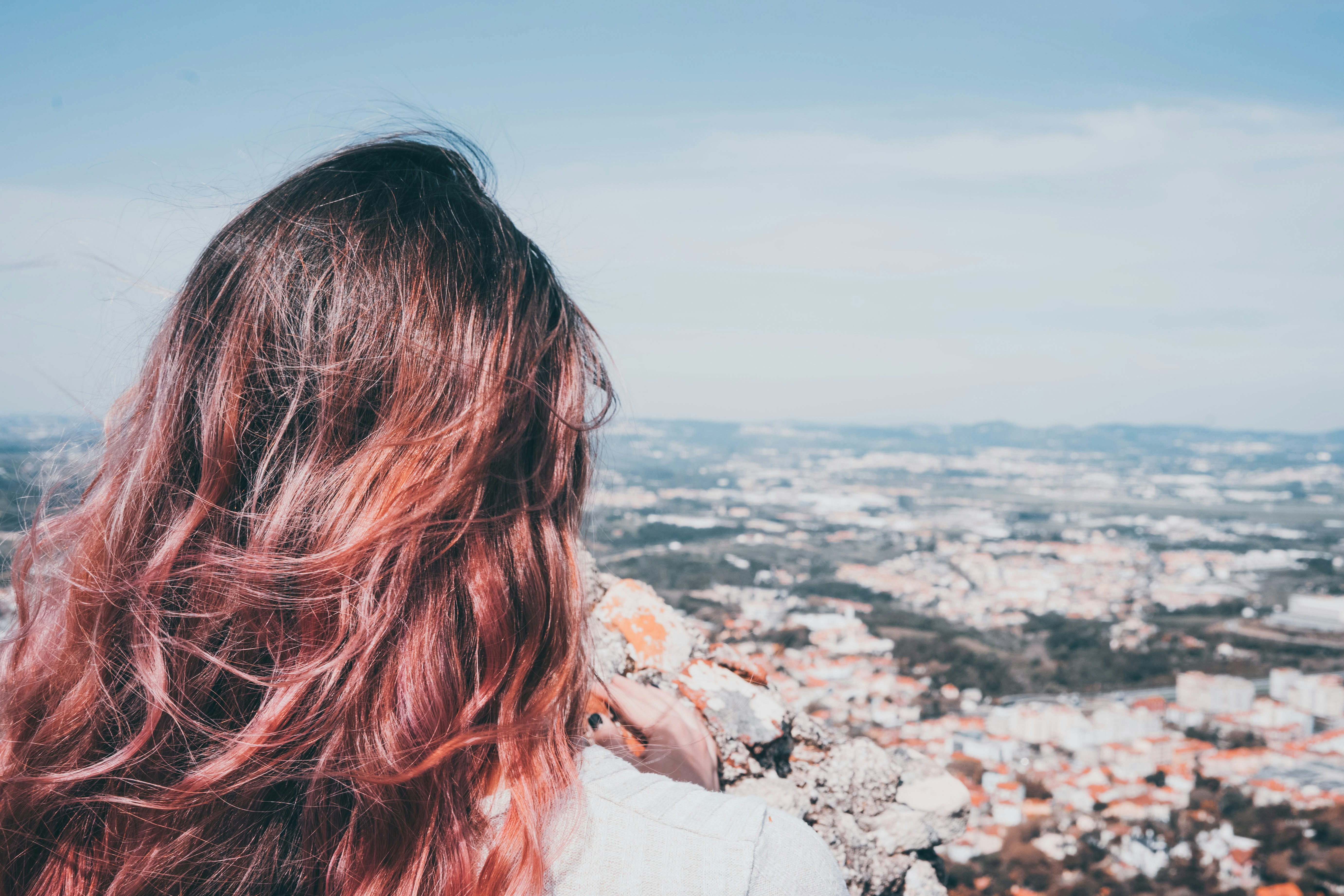 Person with flowing red hair gazing over the expansive landscape from a stone vantage point.