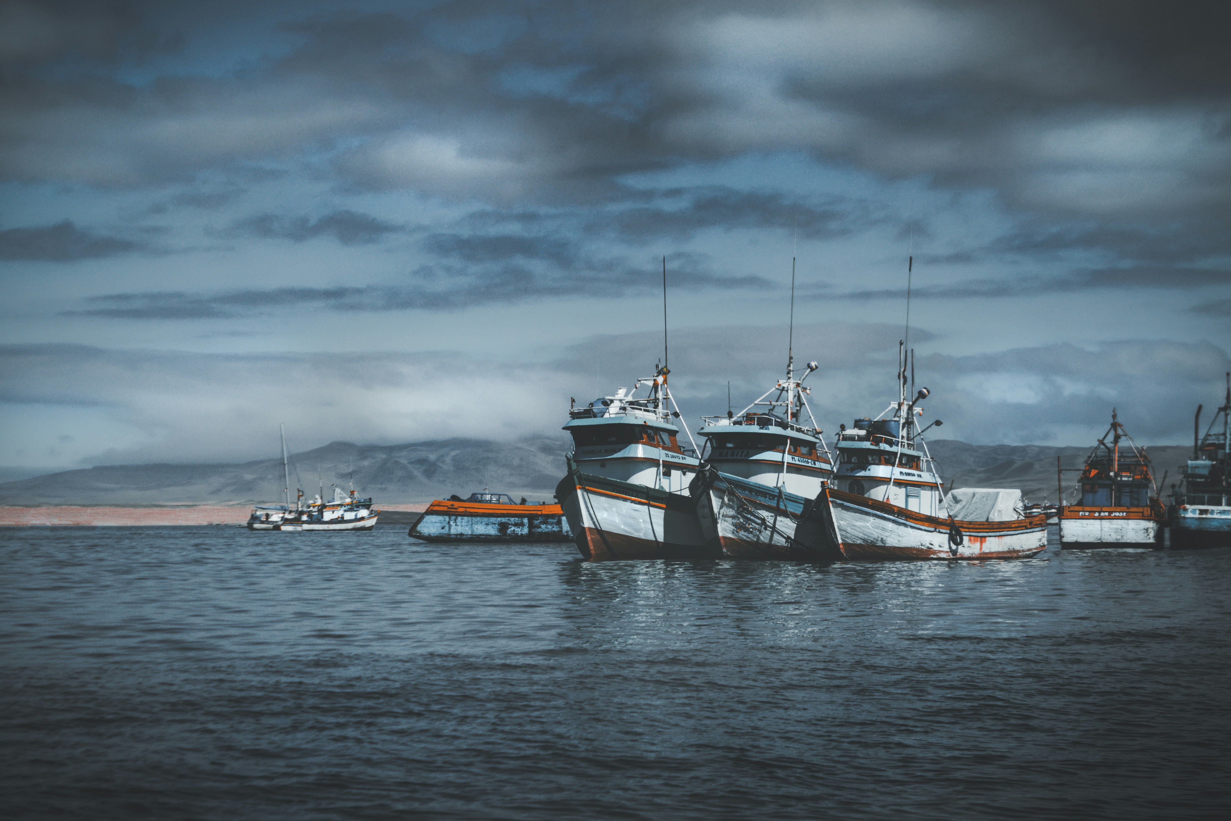 Fishing boats anchored in calm waters beneath a dramatic, cloud-filled sky.