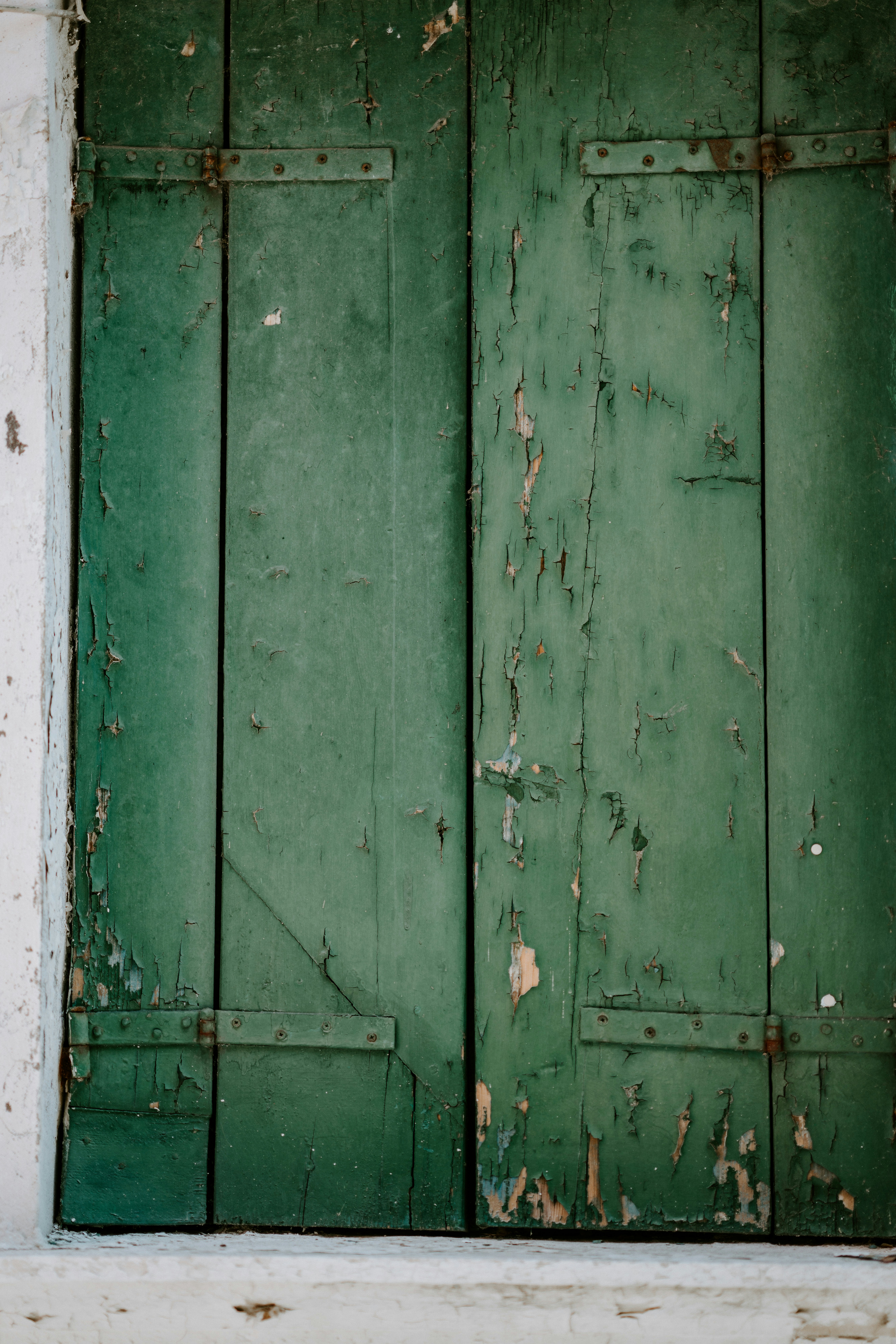Close-up of weathered green shutters with peeling paint and rustic texture, showcasing the passage of time and neglect.