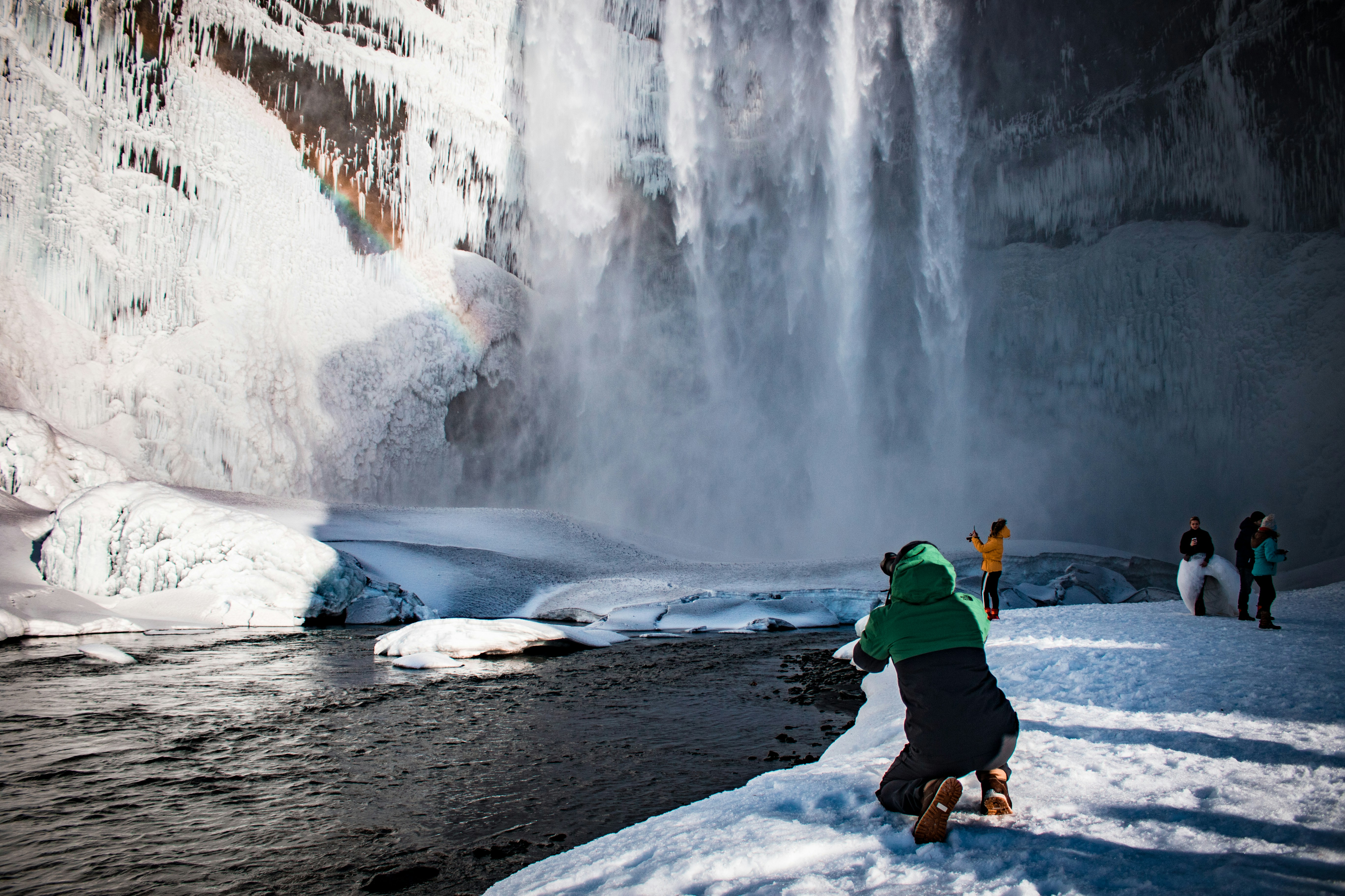 Kneeling by the Frozen Cascade: Green Jacket in a Snowy Vista