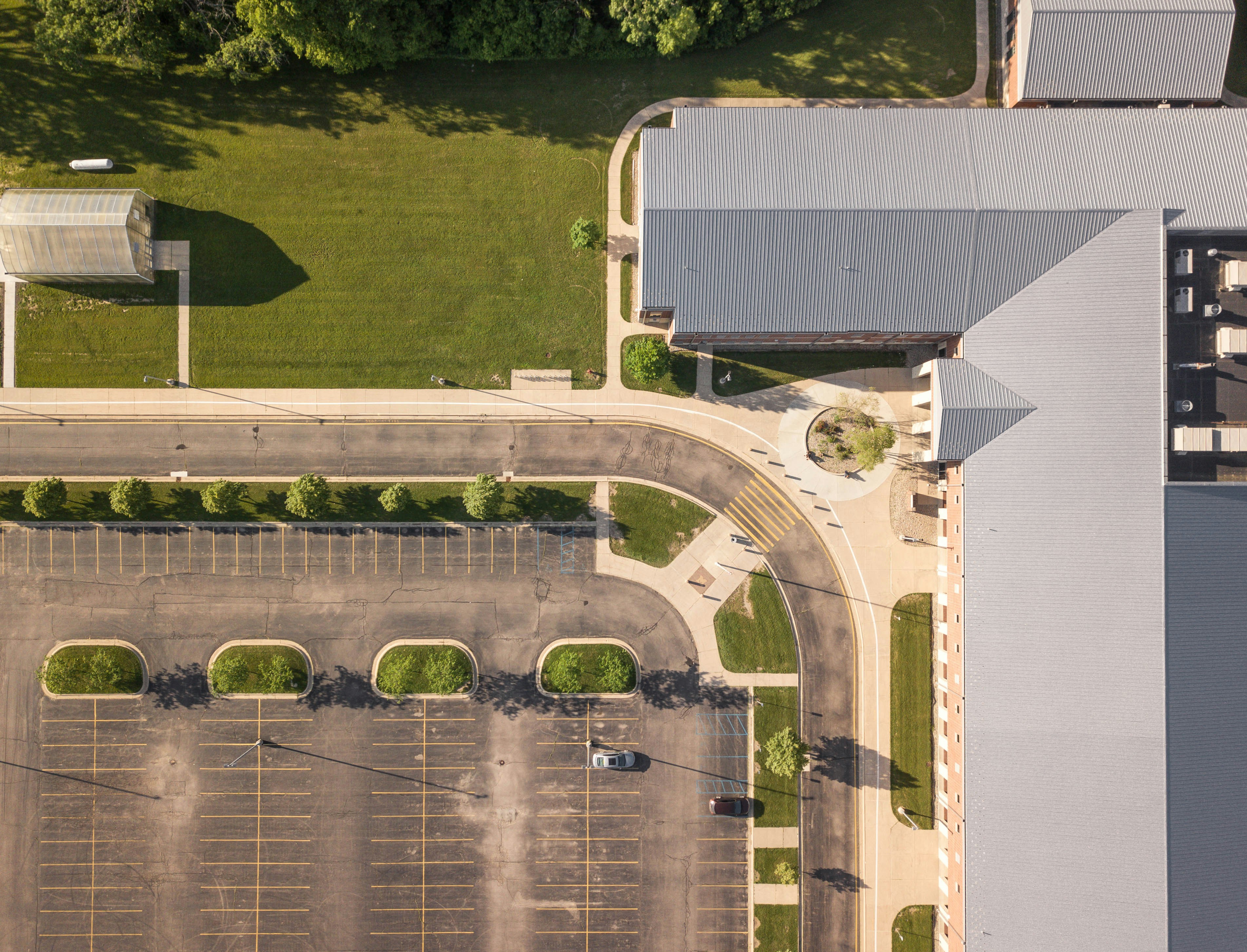 Aerial view of a parking lot adjacent to a modern building, showcasing organized spaces and green landscaping.