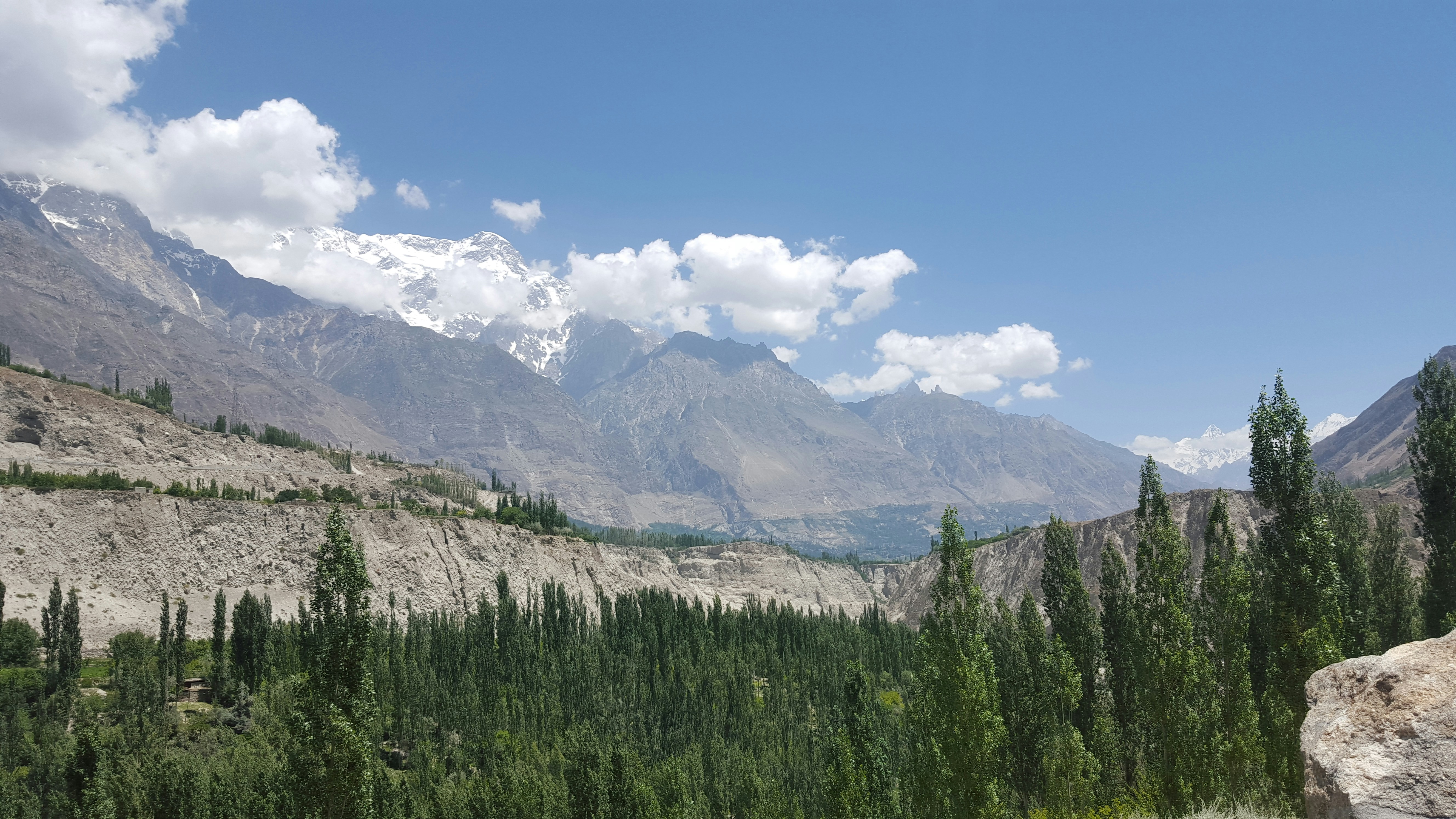 Lush green valley with towering mountains in the background under a blue sky with scattered clouds.