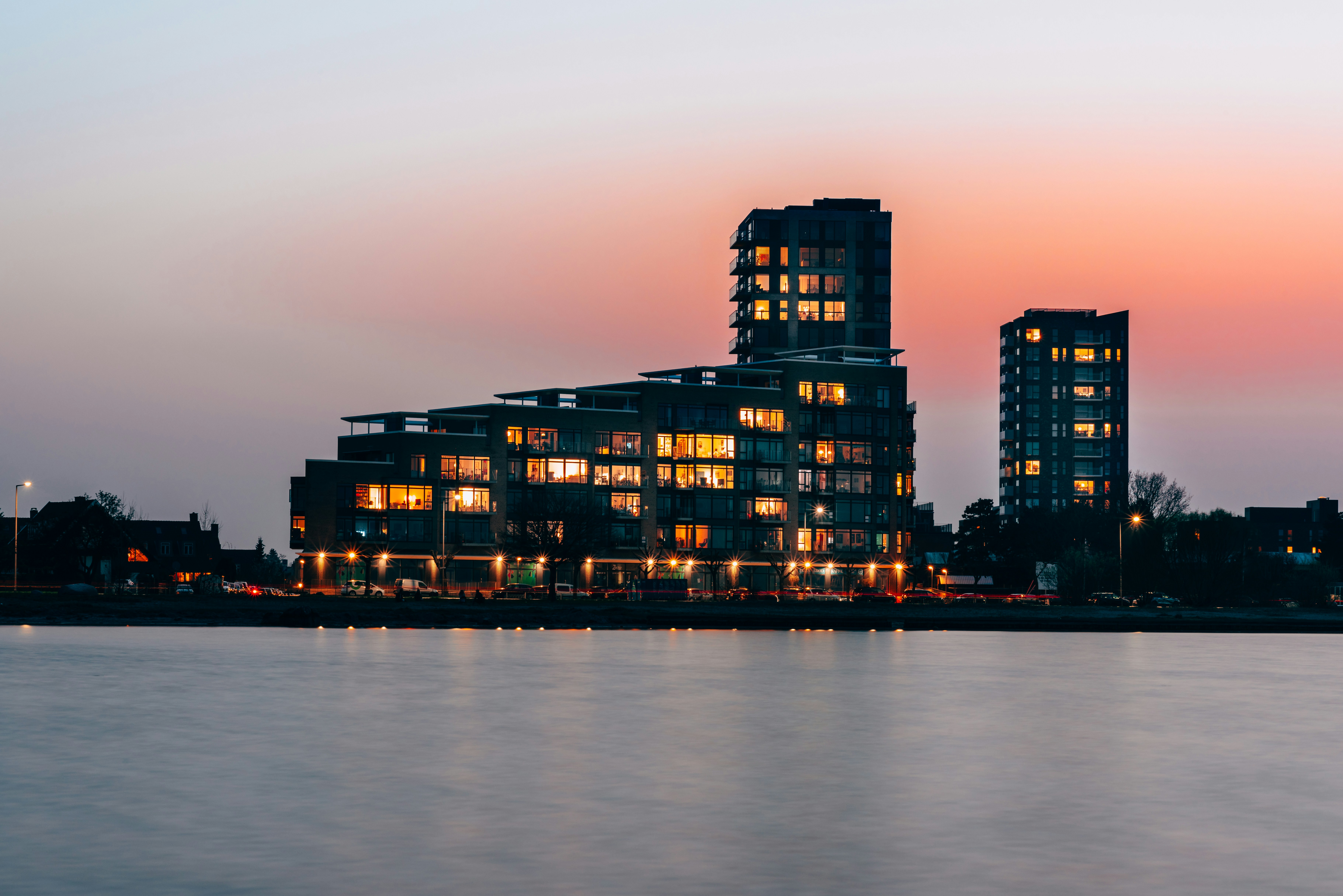 Modern buildings illuminated against a vibrant sunset by the waterfront.