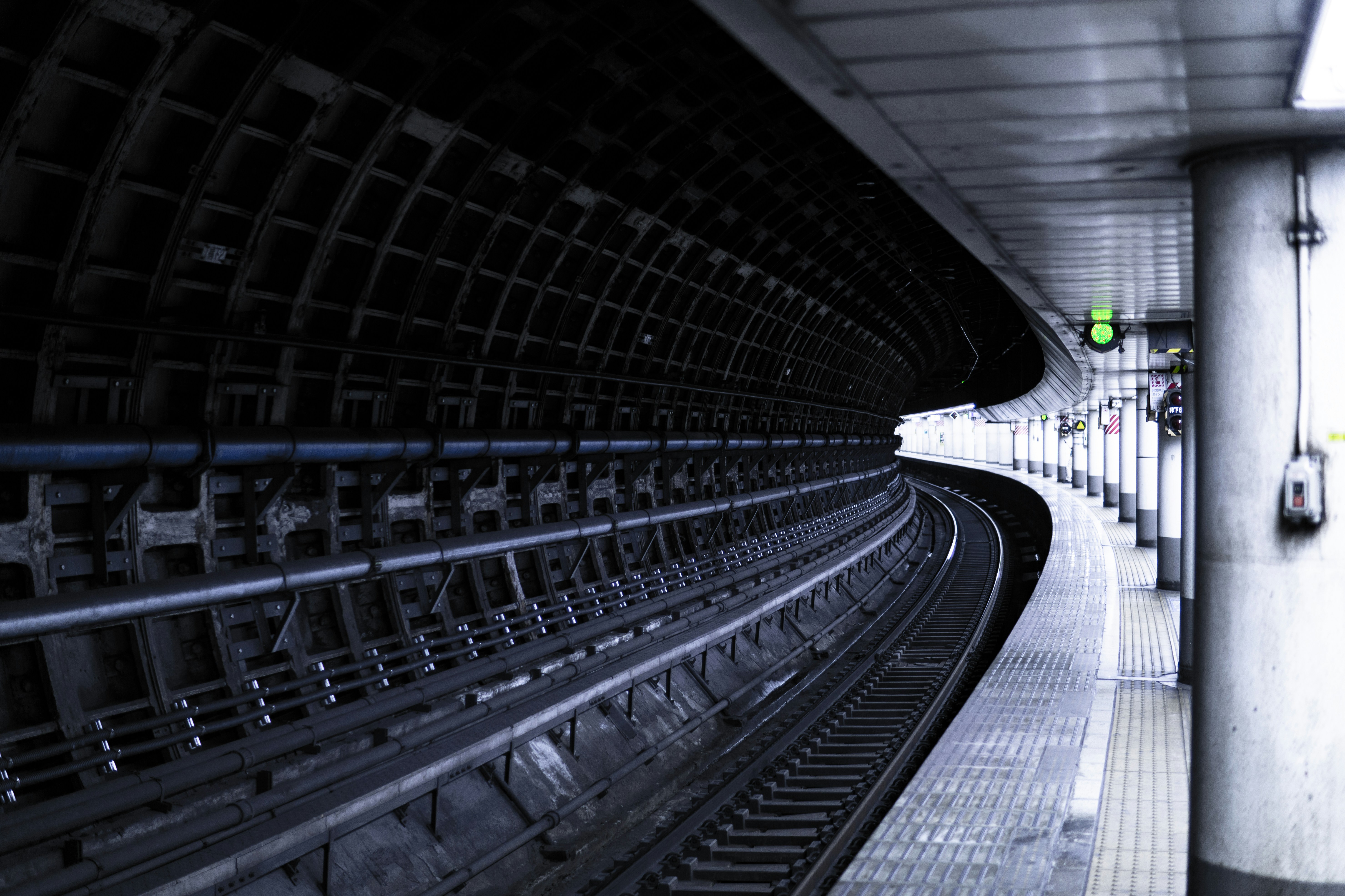 Curved subway platform with distinct architectural lines and a green signal light illuminating the scene.