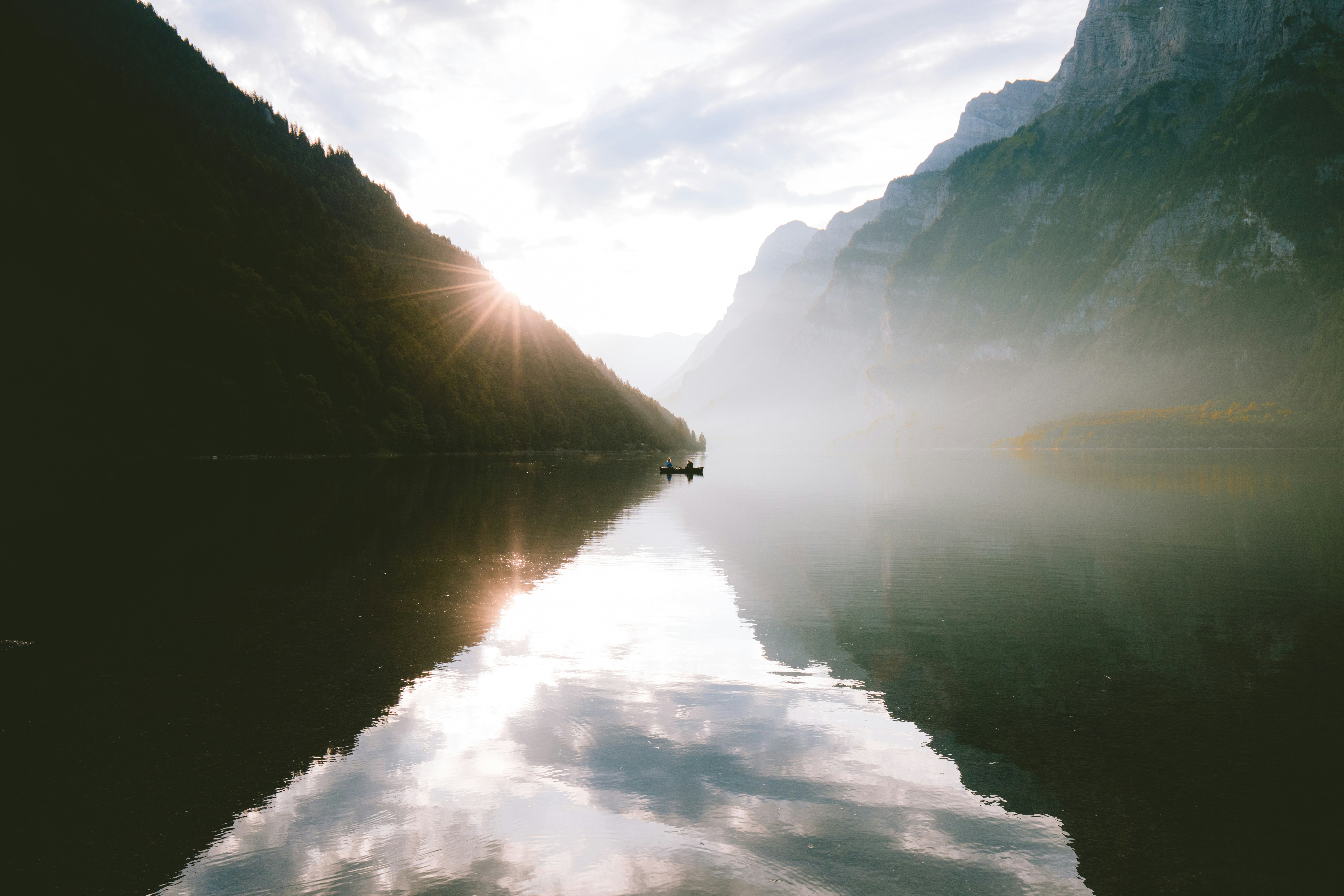 Sunrise casting soft light over a tranquil lake surrounded by misty mountains.