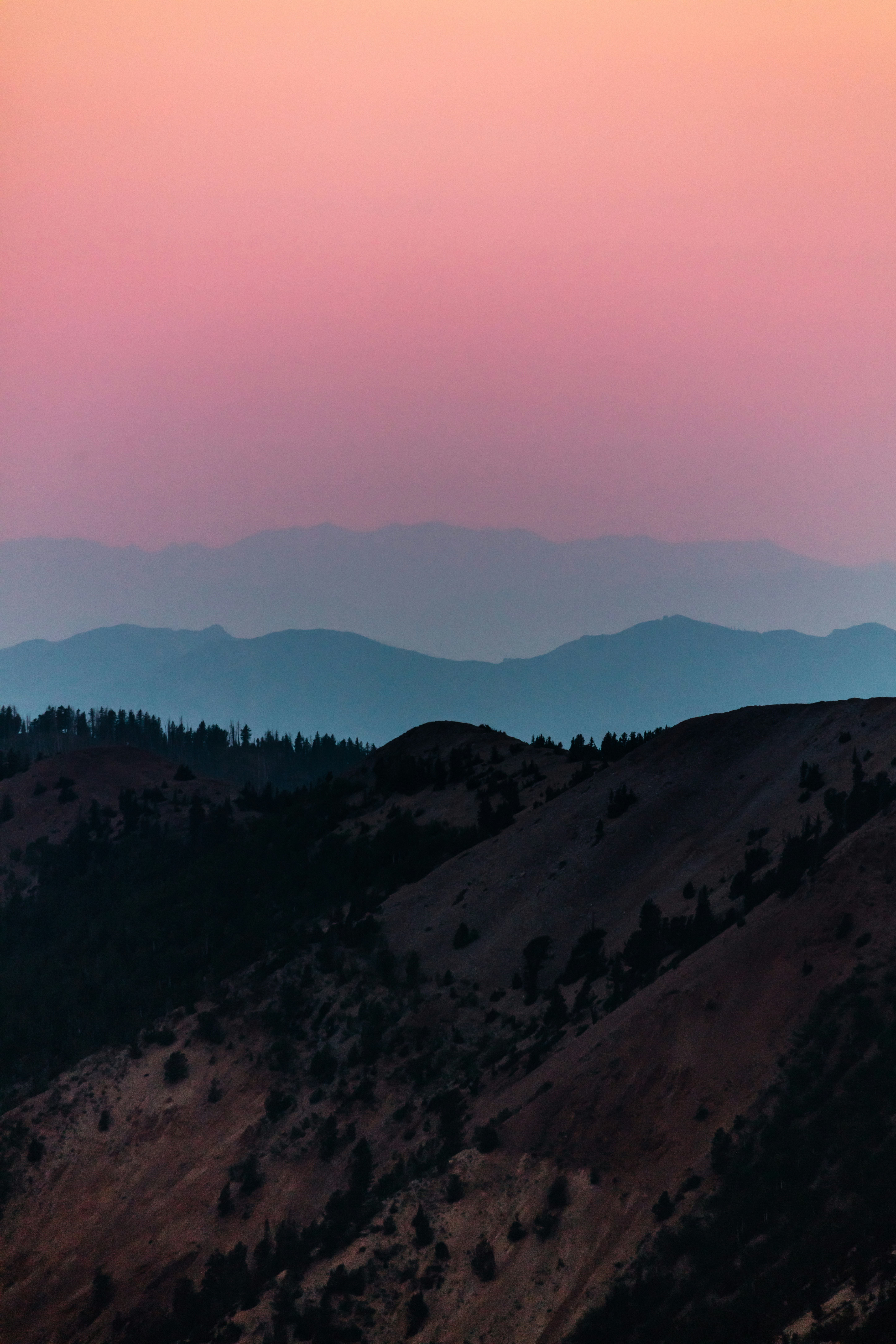 Layers of mountains fade into the horizon under a pastel sky at dusk, showcasing the tranquil transition from day to night.