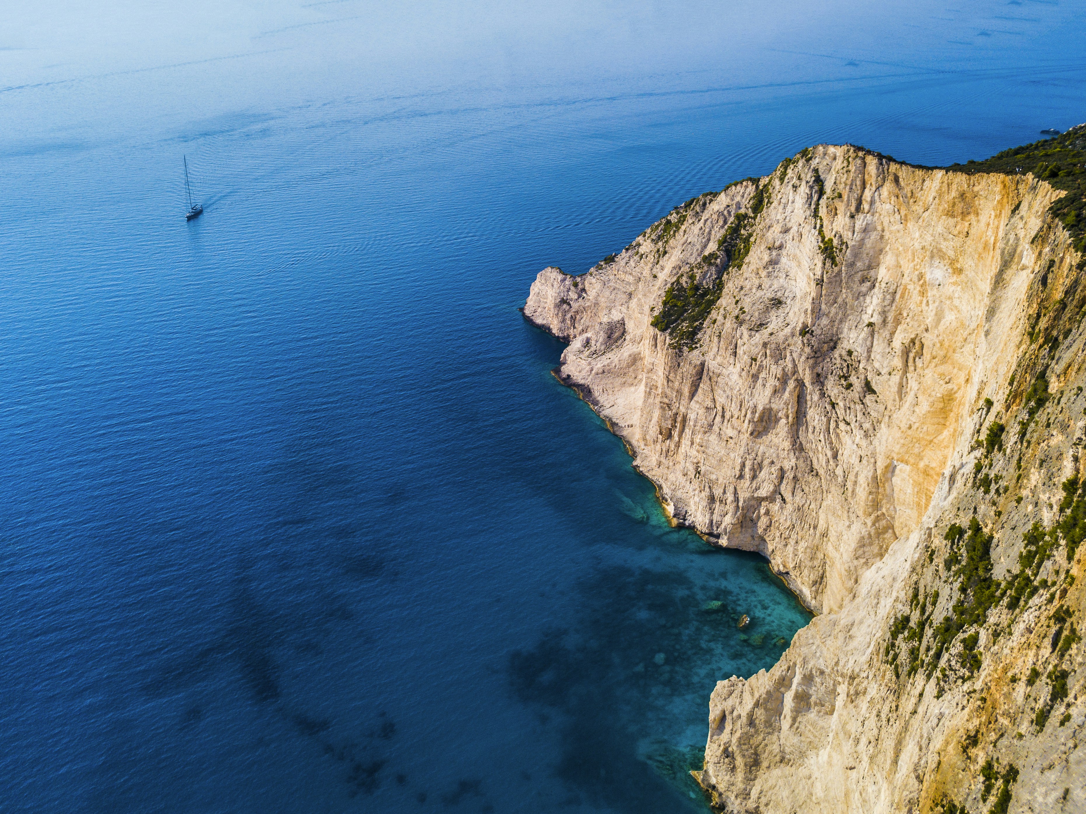 Steep rocky cliffs meet the deep blue sea under a clear sky, captured from above.