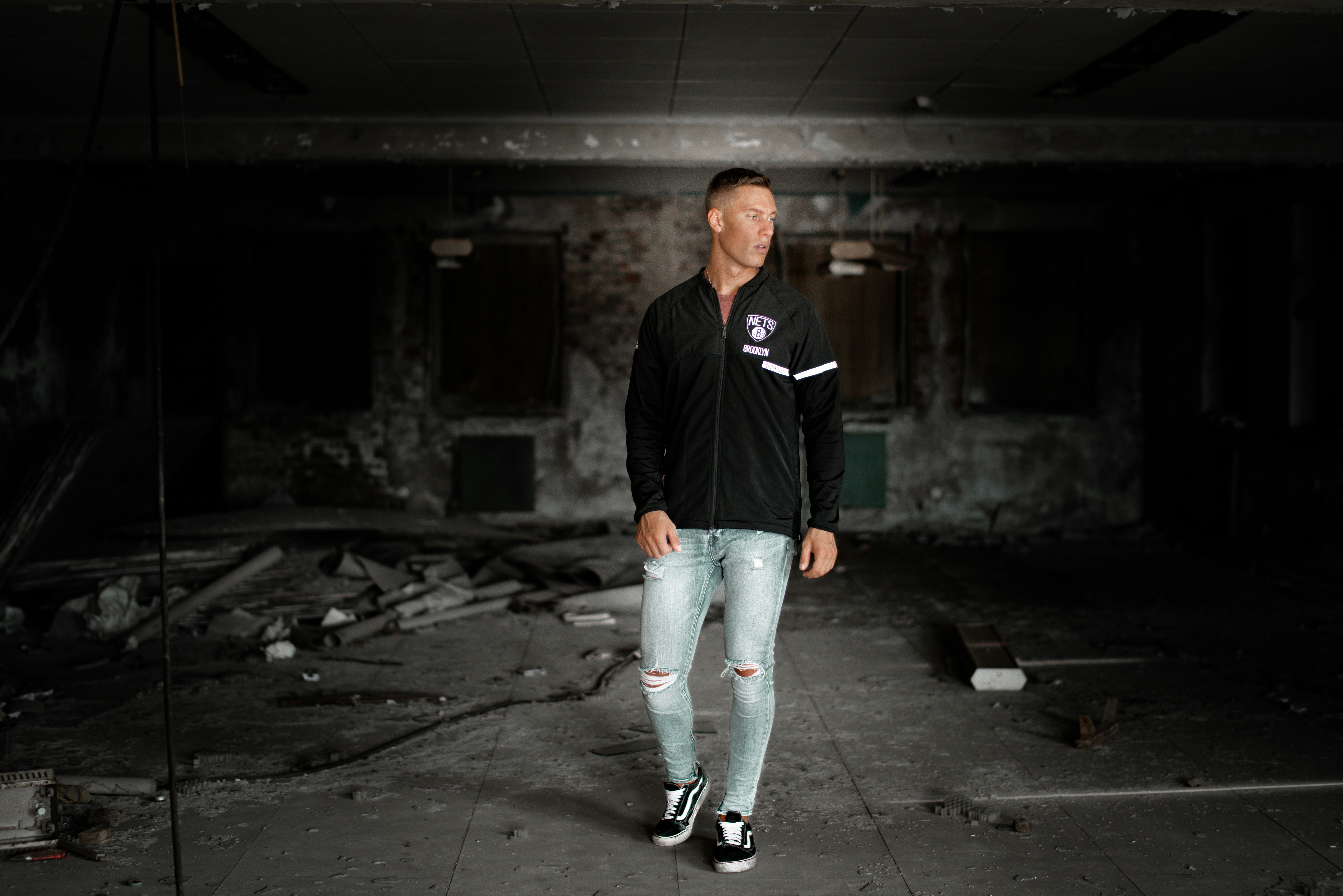 A lone figure walks through a dilapidated interior, surrounded by debris and shadows, embodying a sense of solitude and exploration.