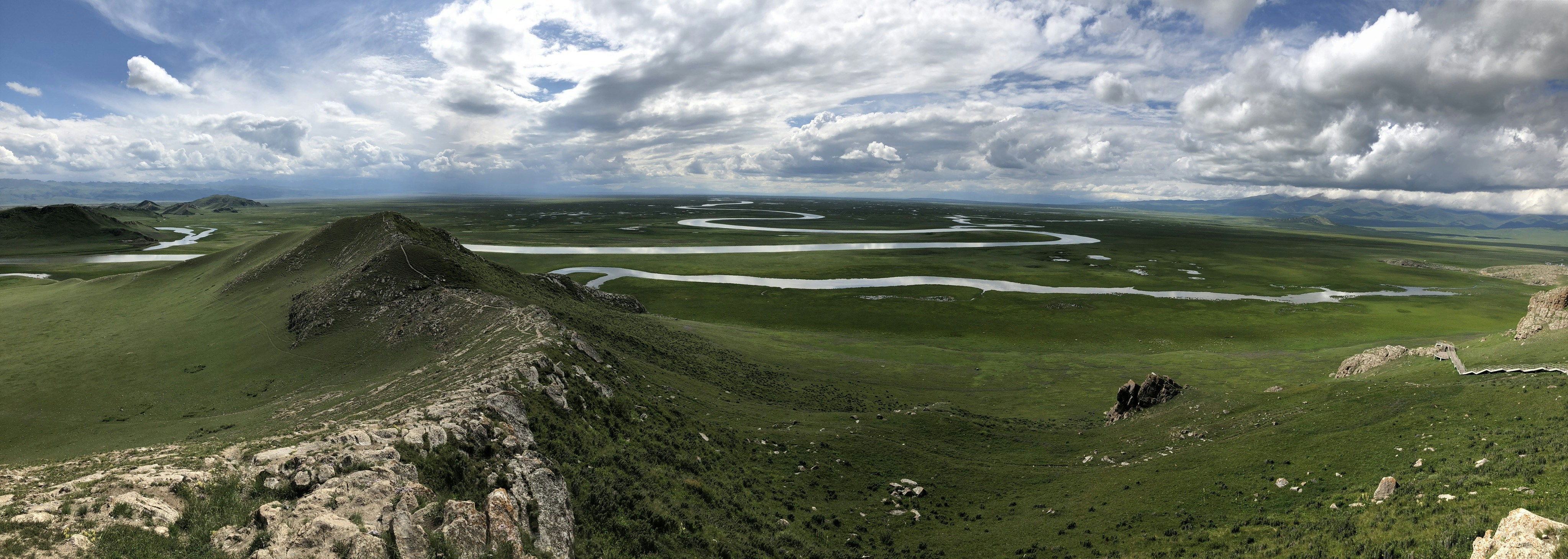 Vast green landscape with a winding river under a dramatic cloudy sky.