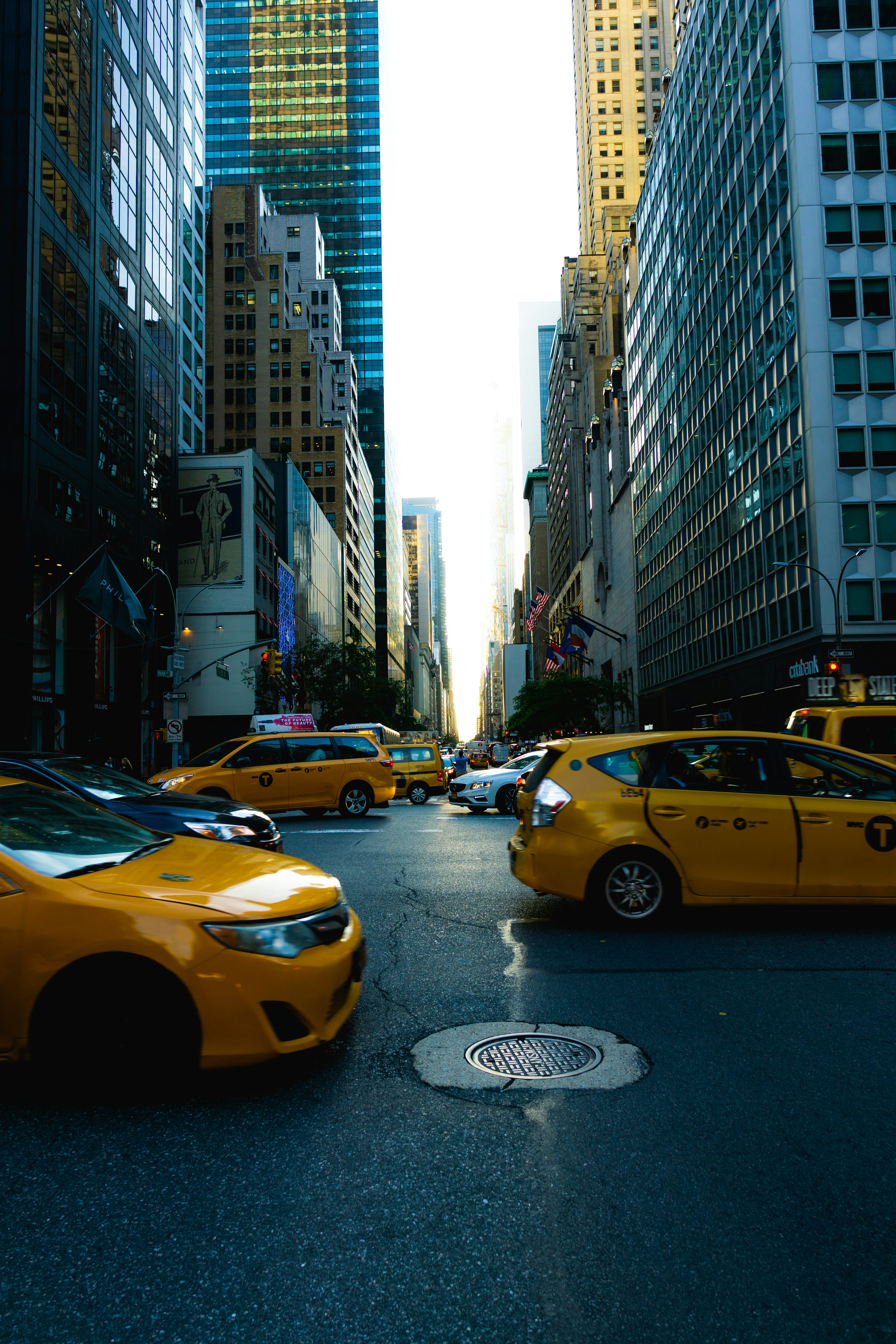 Yellow taxis navigate a bustling city intersection surrounded by towering skyscrapers.
