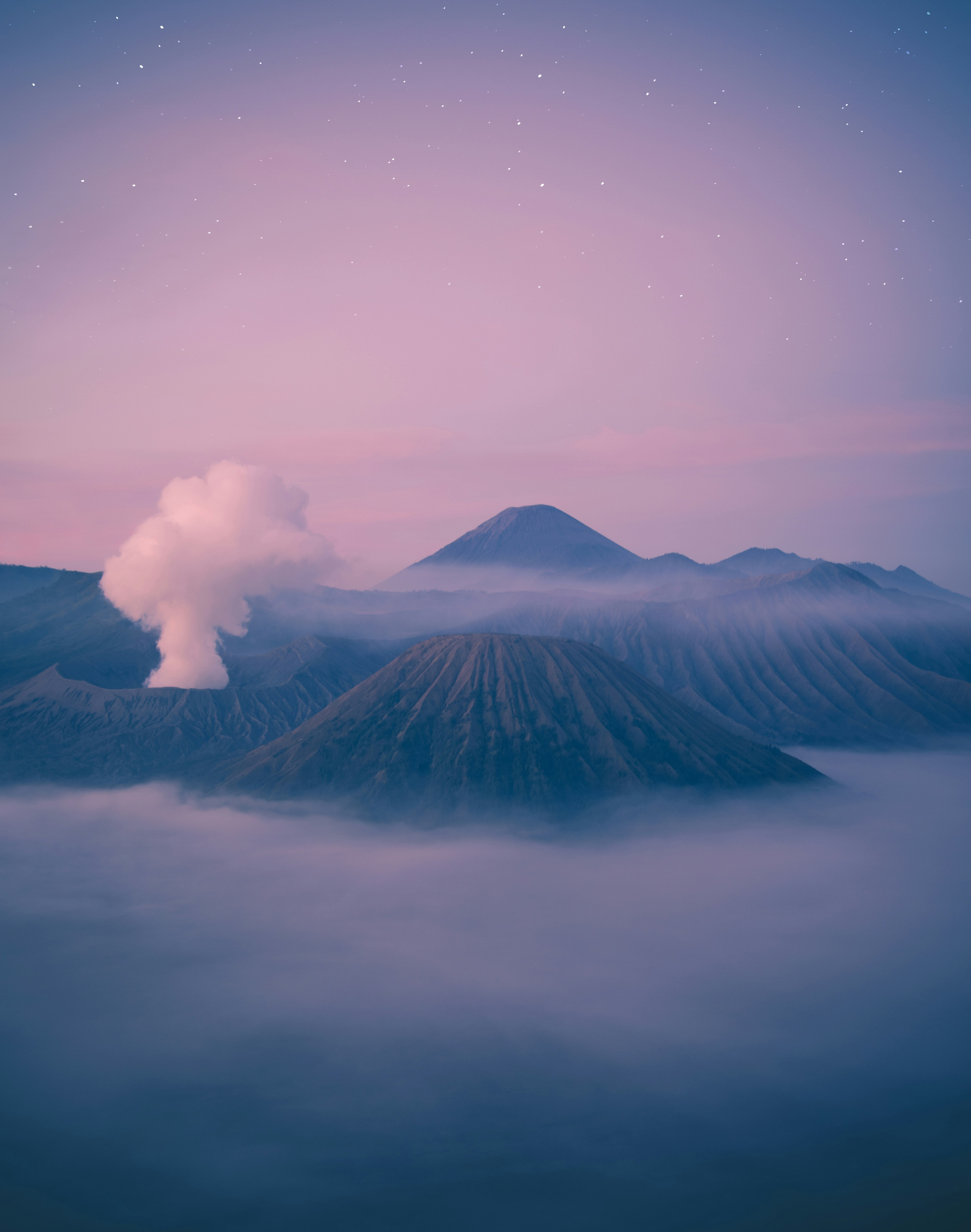 Volcanic peaks rise through a sea of mist under a dawn sky.